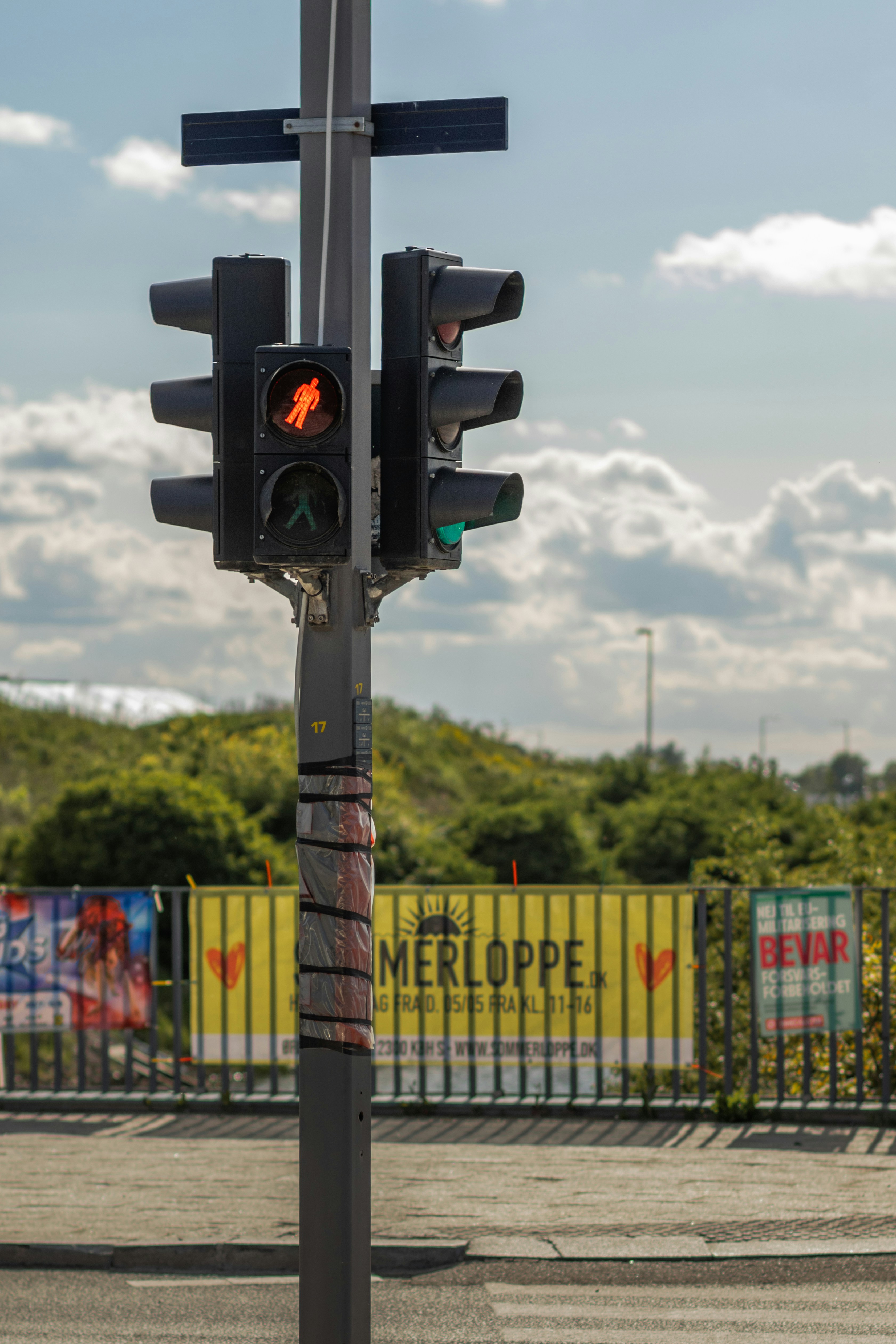 Orange Pedestrian Signal Amid Bannered Fence Under a Bright Sky