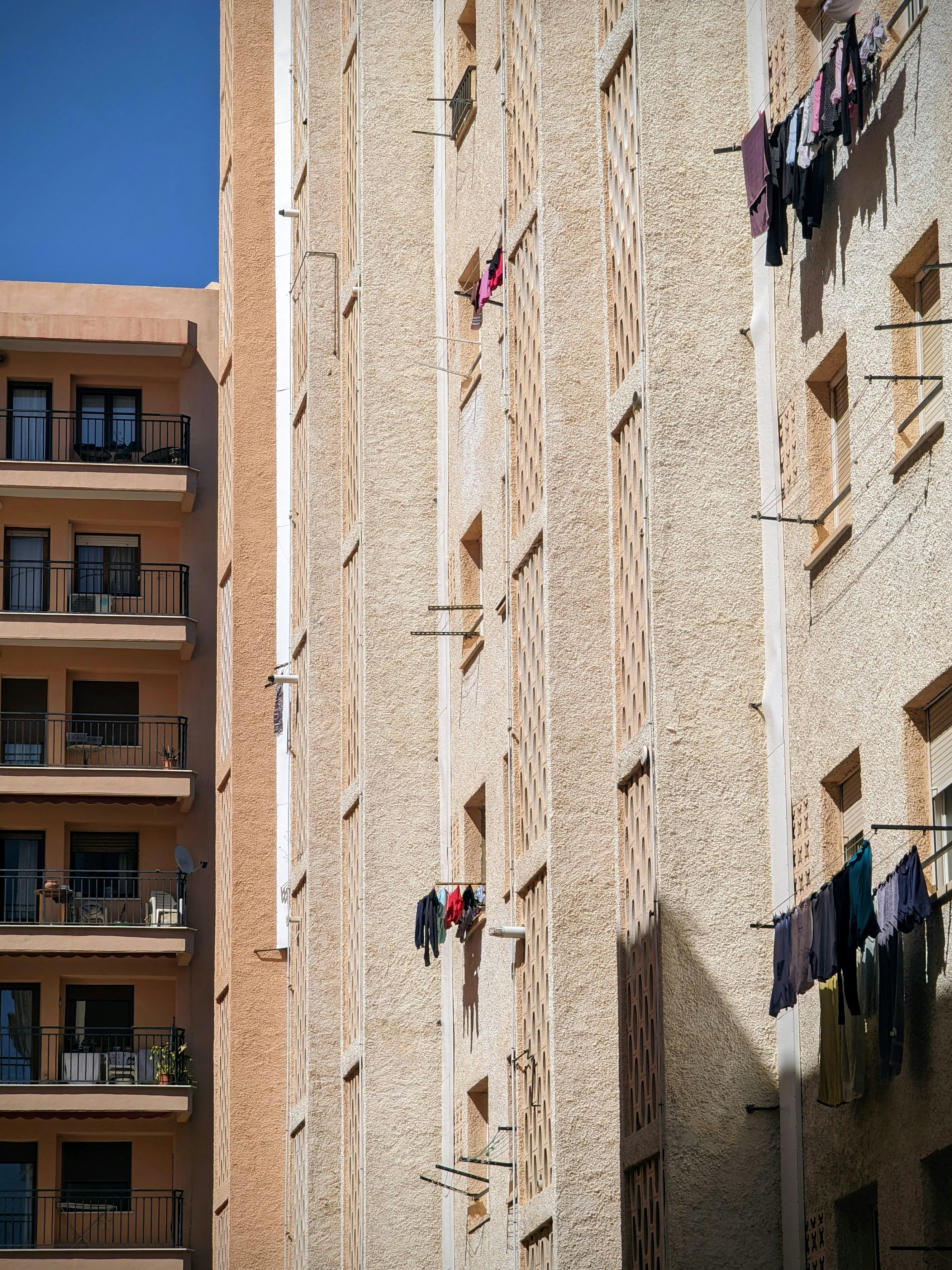 Clothes hang from balconies and lines between beige apartment buildings, showcasing a slice of urban living. The scene captures the interplay of architecture and everyday activities.