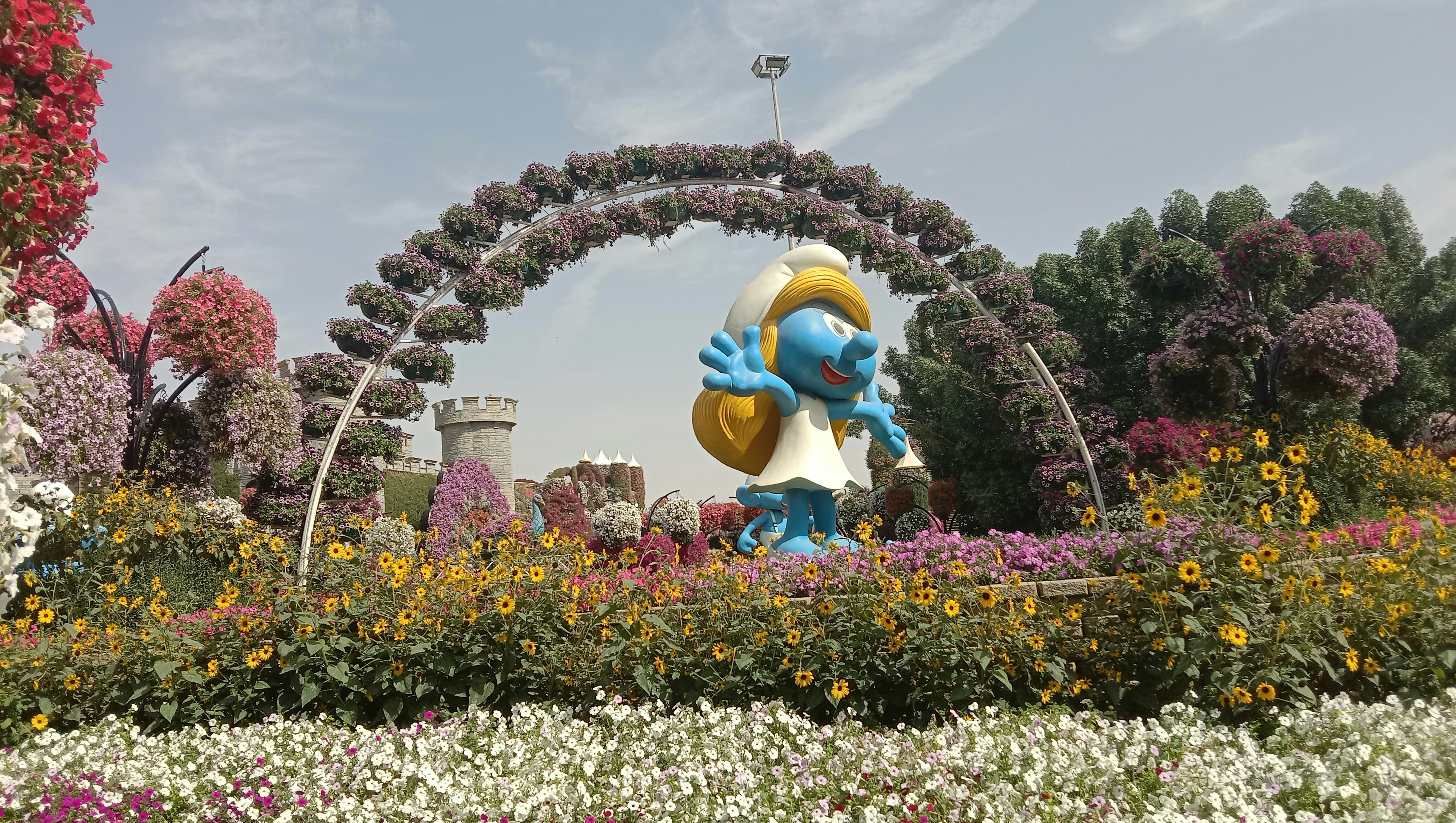 A blue smurf statue in a flower garden photo – Free Miracle garden ...