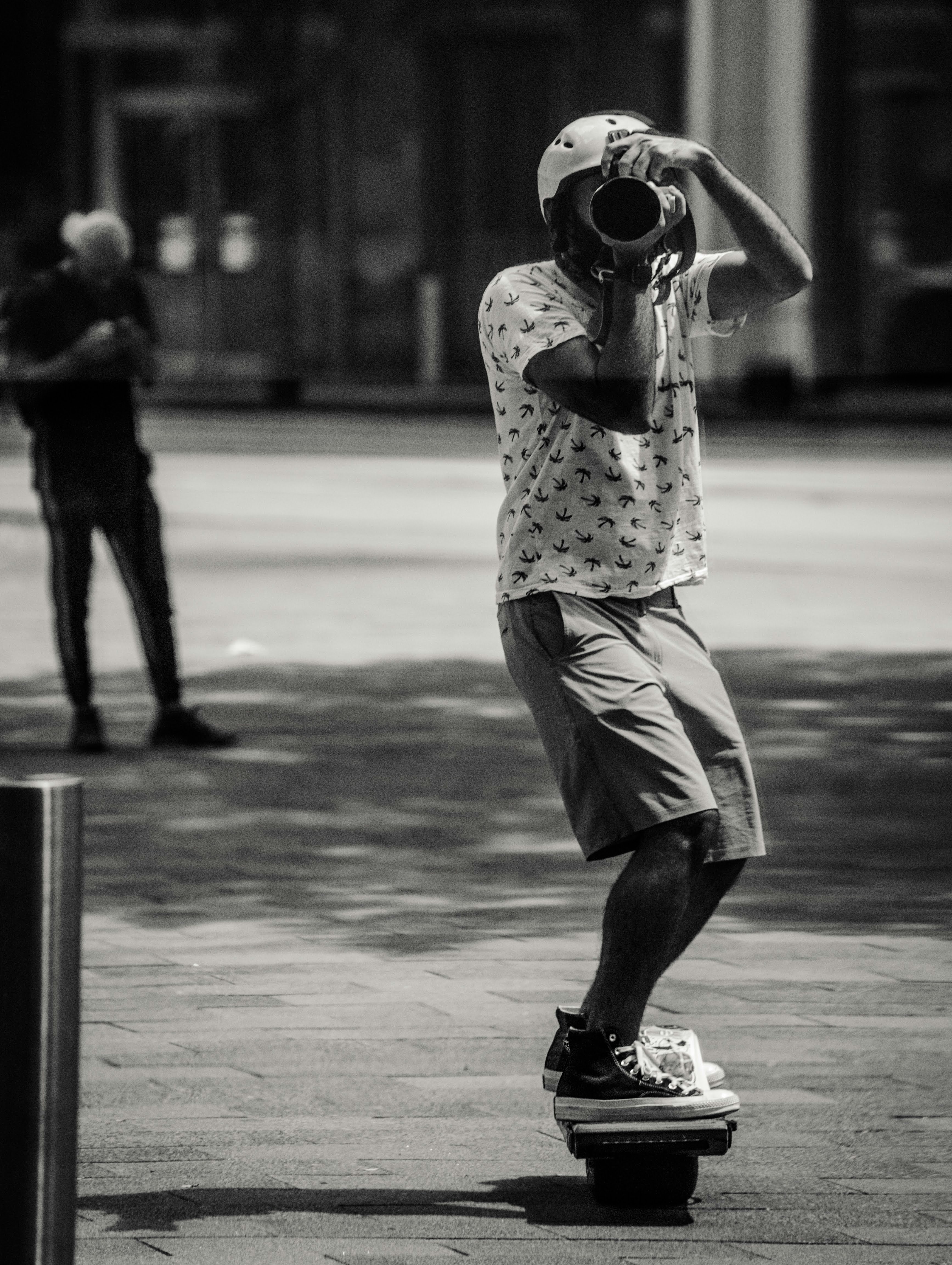 Monochrome Maneuver: Helmeted Photographer Balances on a Skateboard