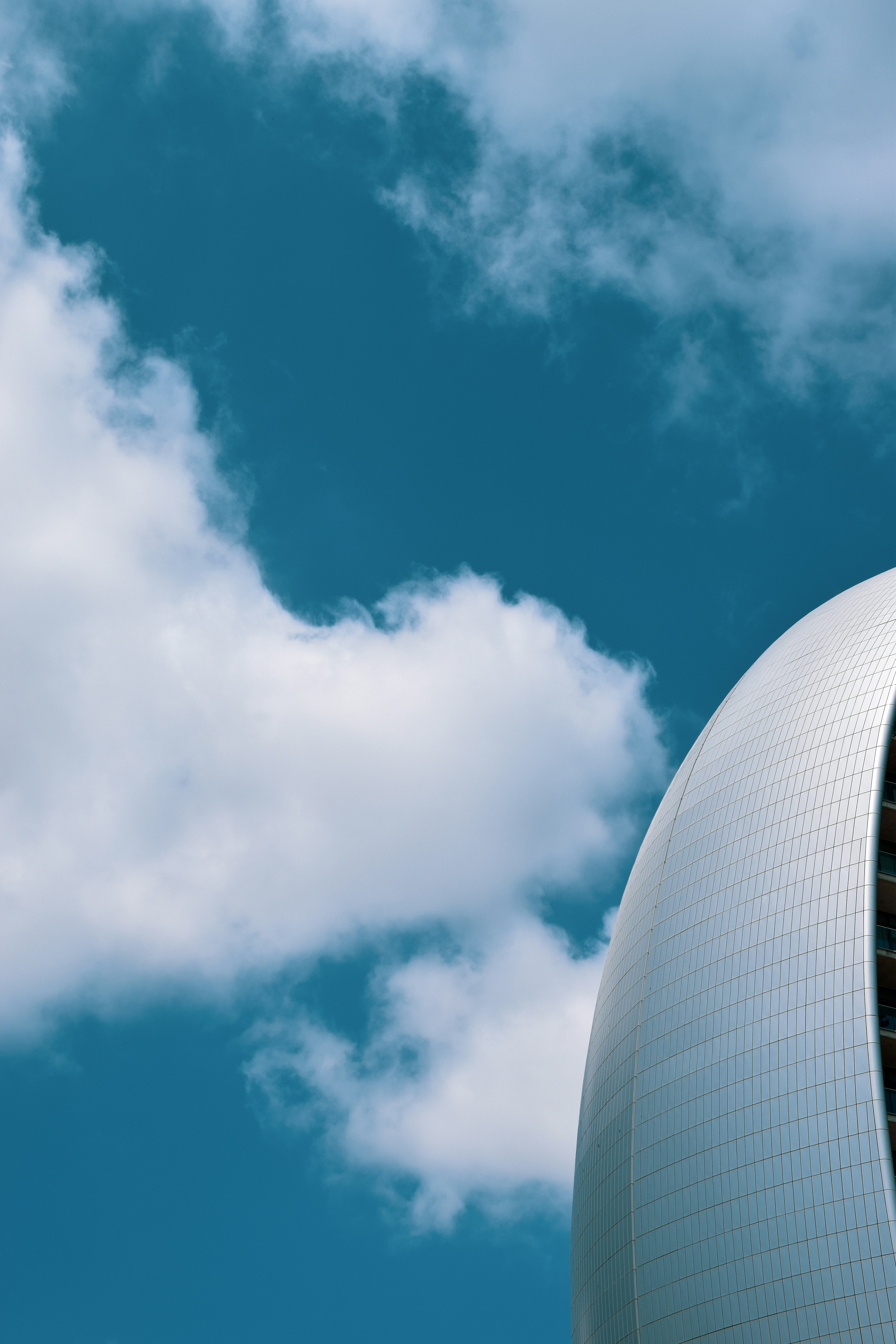 Sleek, modern architectural structure partially obscured by fluffy clouds in a vibrant blue sky.