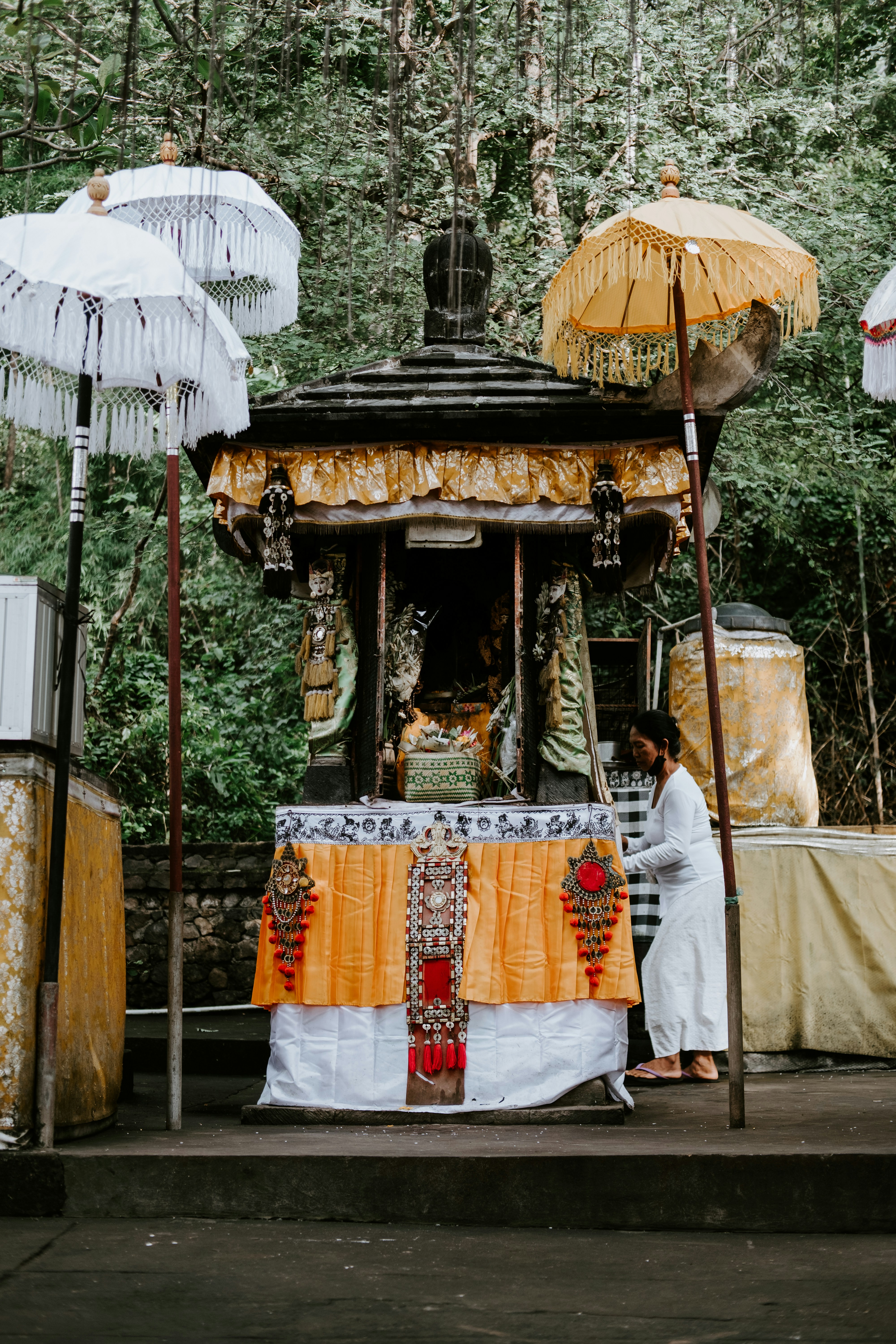 Traditional Balinese shrine adorned with vibrant offerings and parasols surrounded by lush greenery.