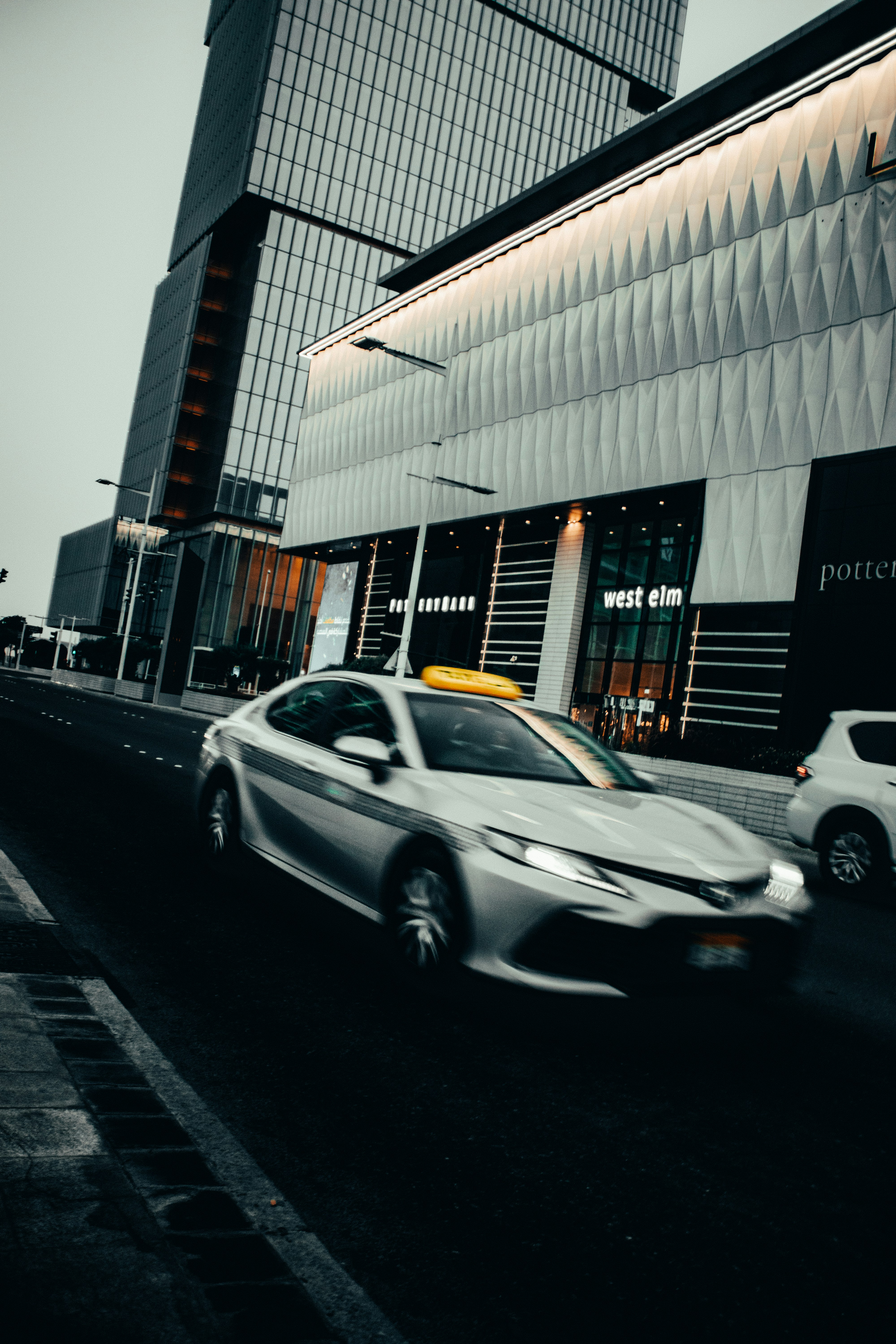 A white car driving down a street next to a tall building photo – Free ...