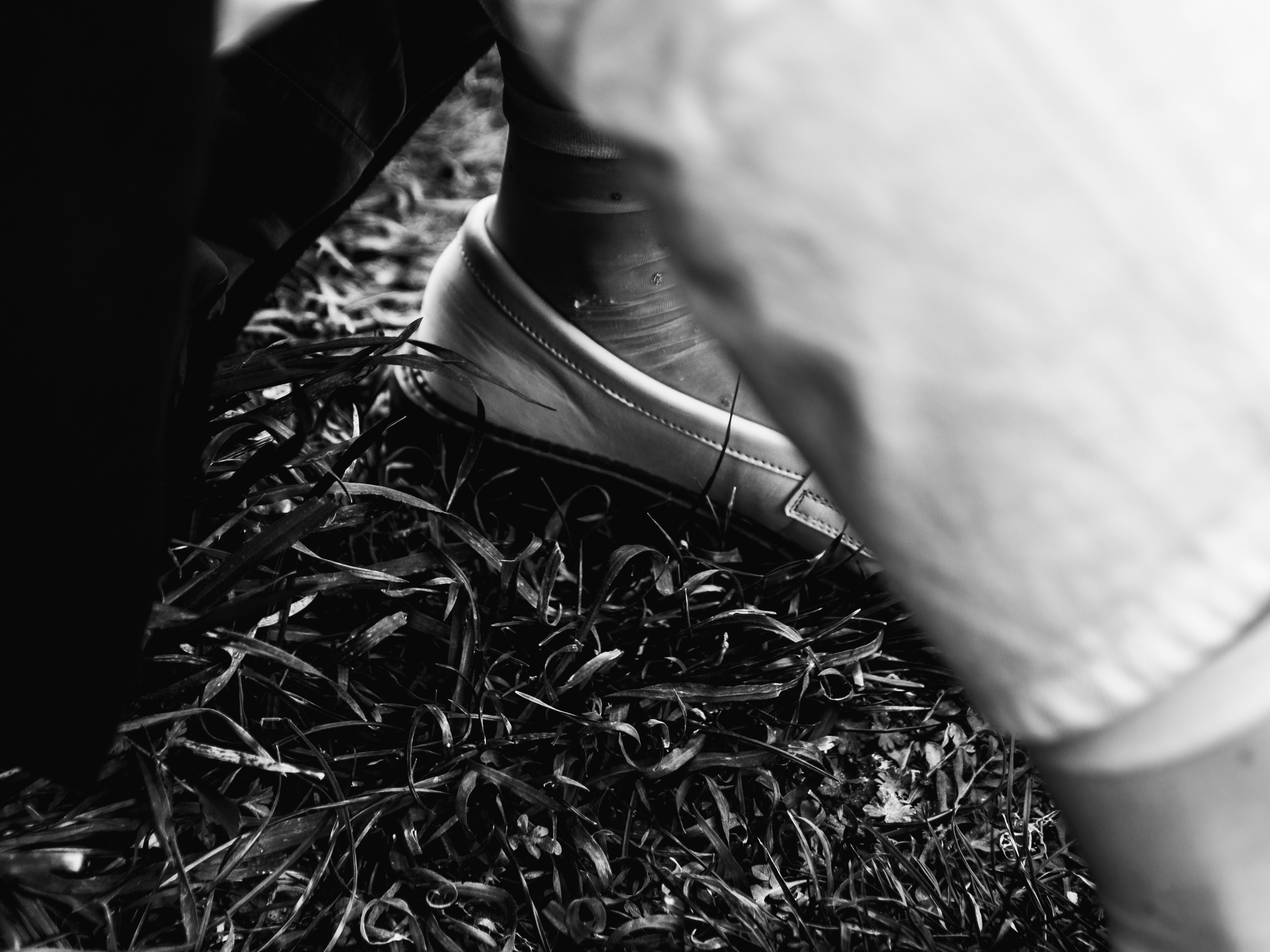 Close-up of feet on grass, showcasing textures and contrasting light in a monochrome setting.