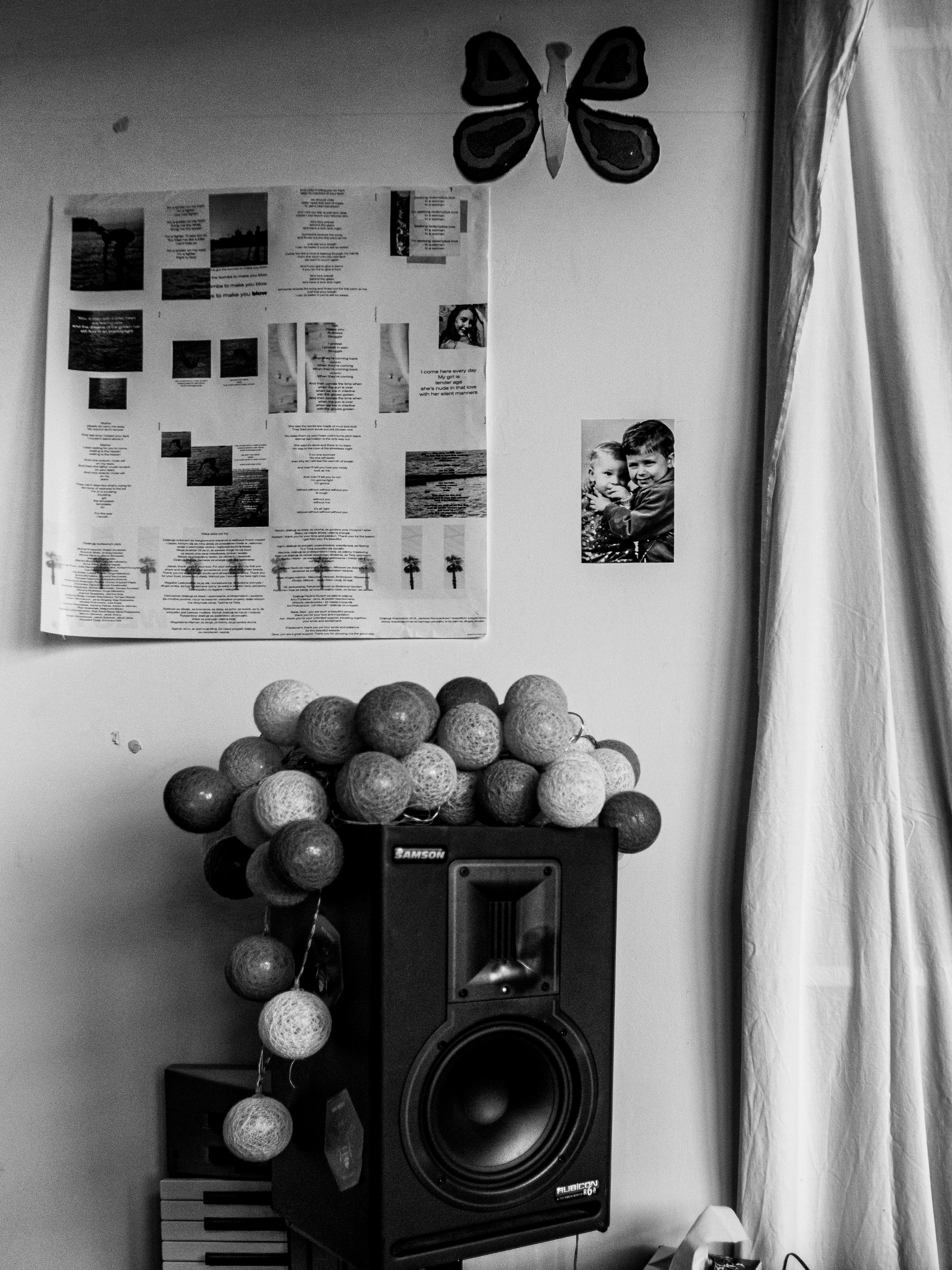 A black-and-white interior scene featuring a speaker adorned with colorful decorative balls, surrounded by a wall of poetry and personal photographs.