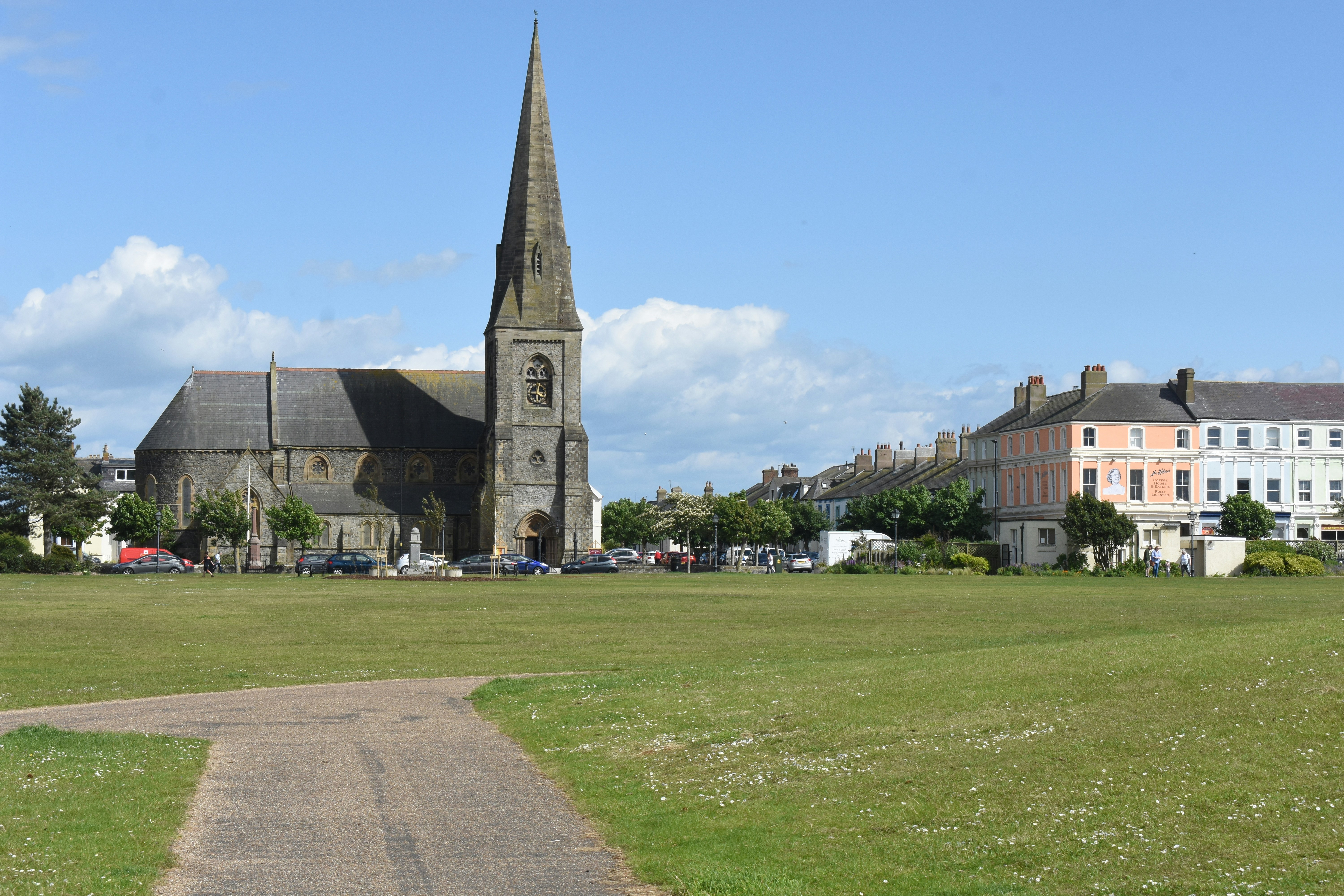 Historic church with a tall spire surrounded by lush green grass and residential buildings in the background.