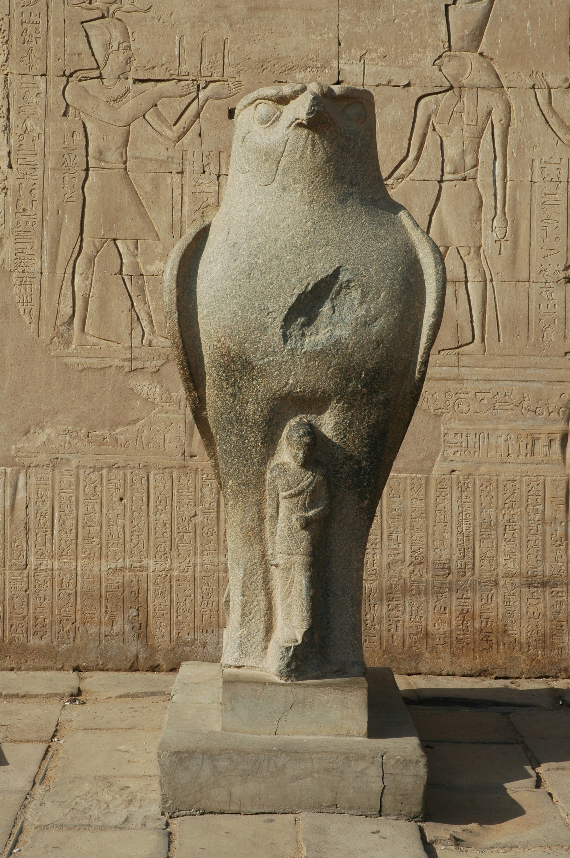 a statue of a bird on a pedestal in front of a wall