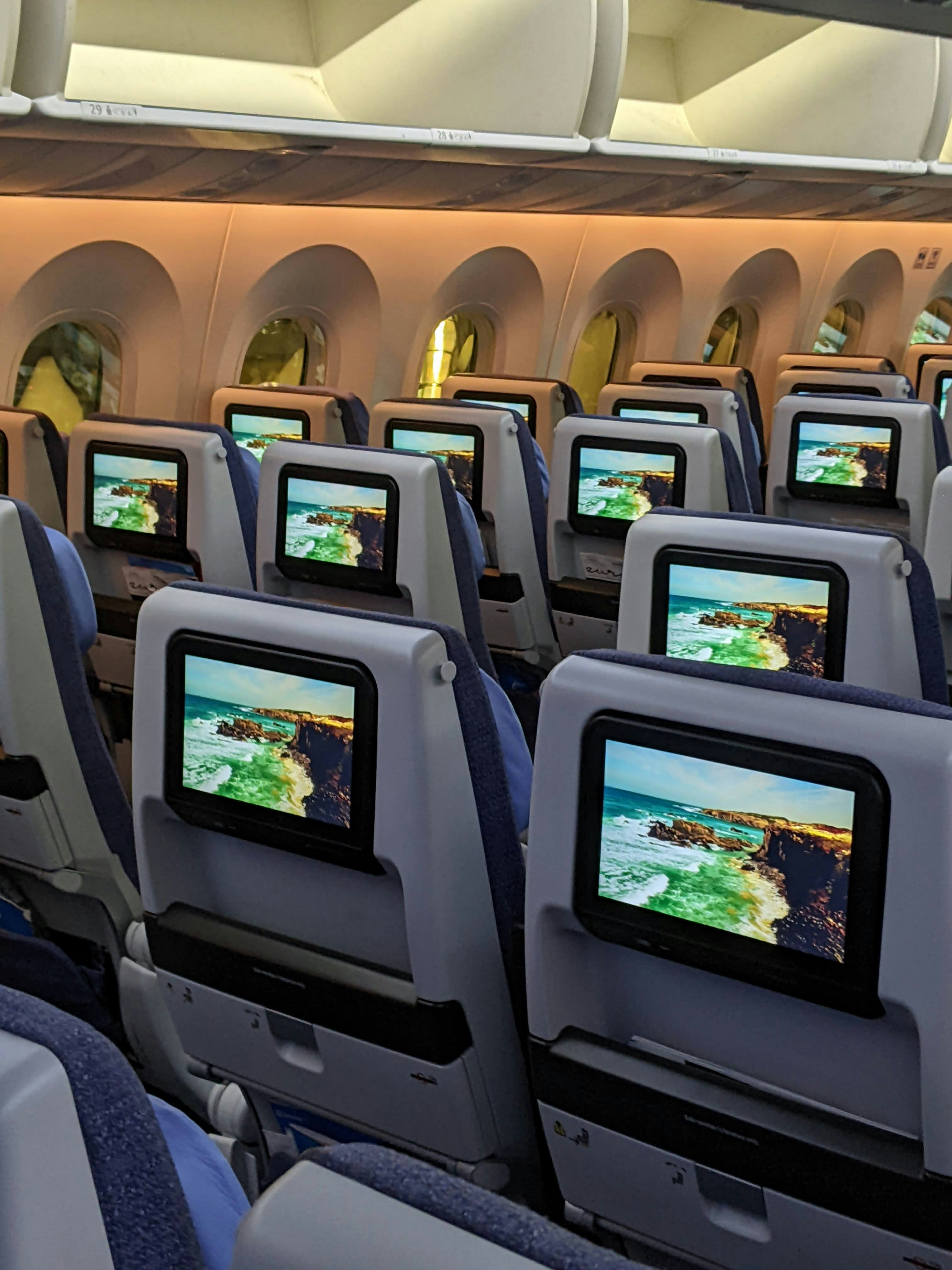 Windowless Voyage: In-Flight Screens Glimmer Across a Sea of Economy