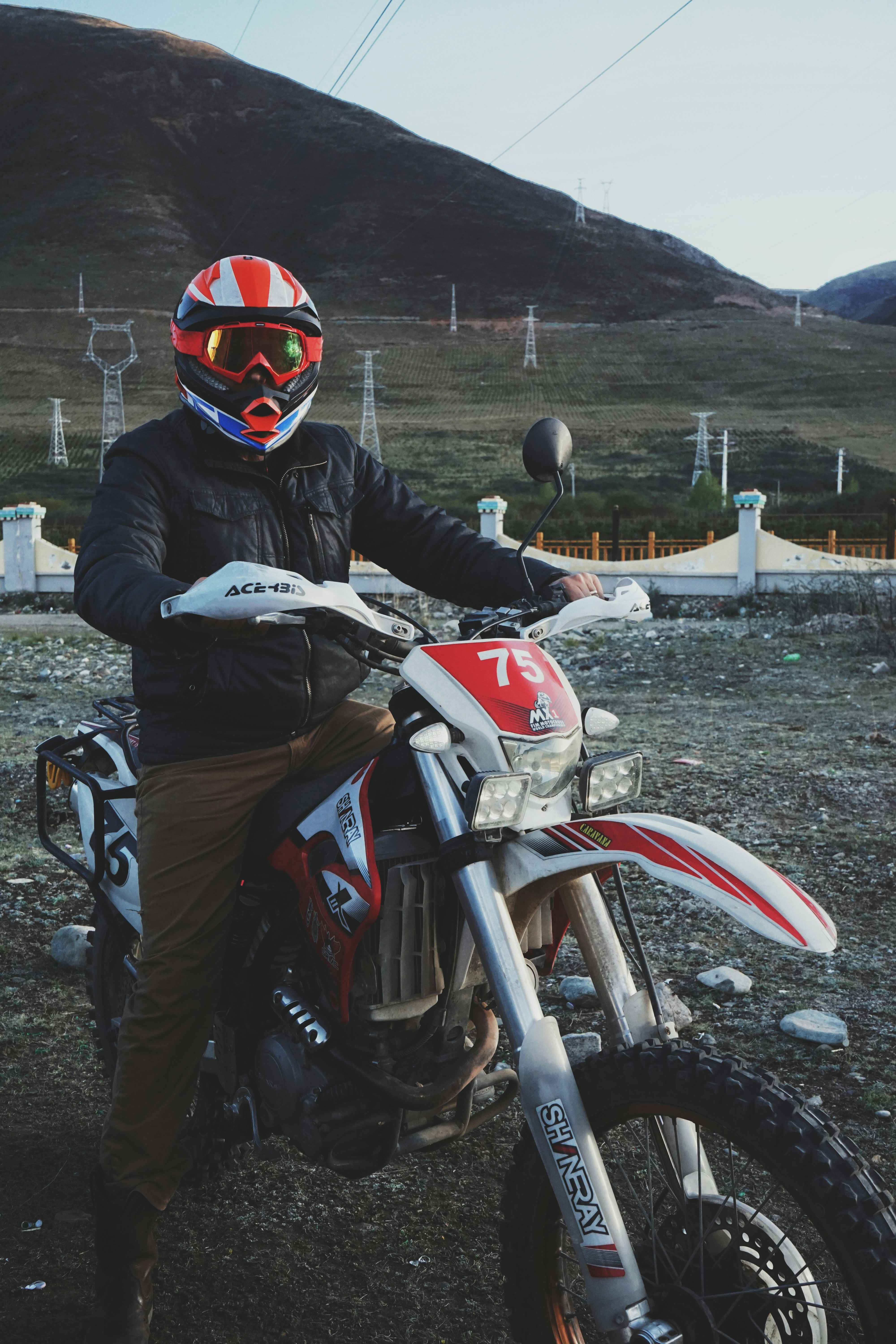 A motorcyclist clad in protective gear sits confidently on a dirt bike against a mountainous backdrop, showcasing the thrill of off-road riding.