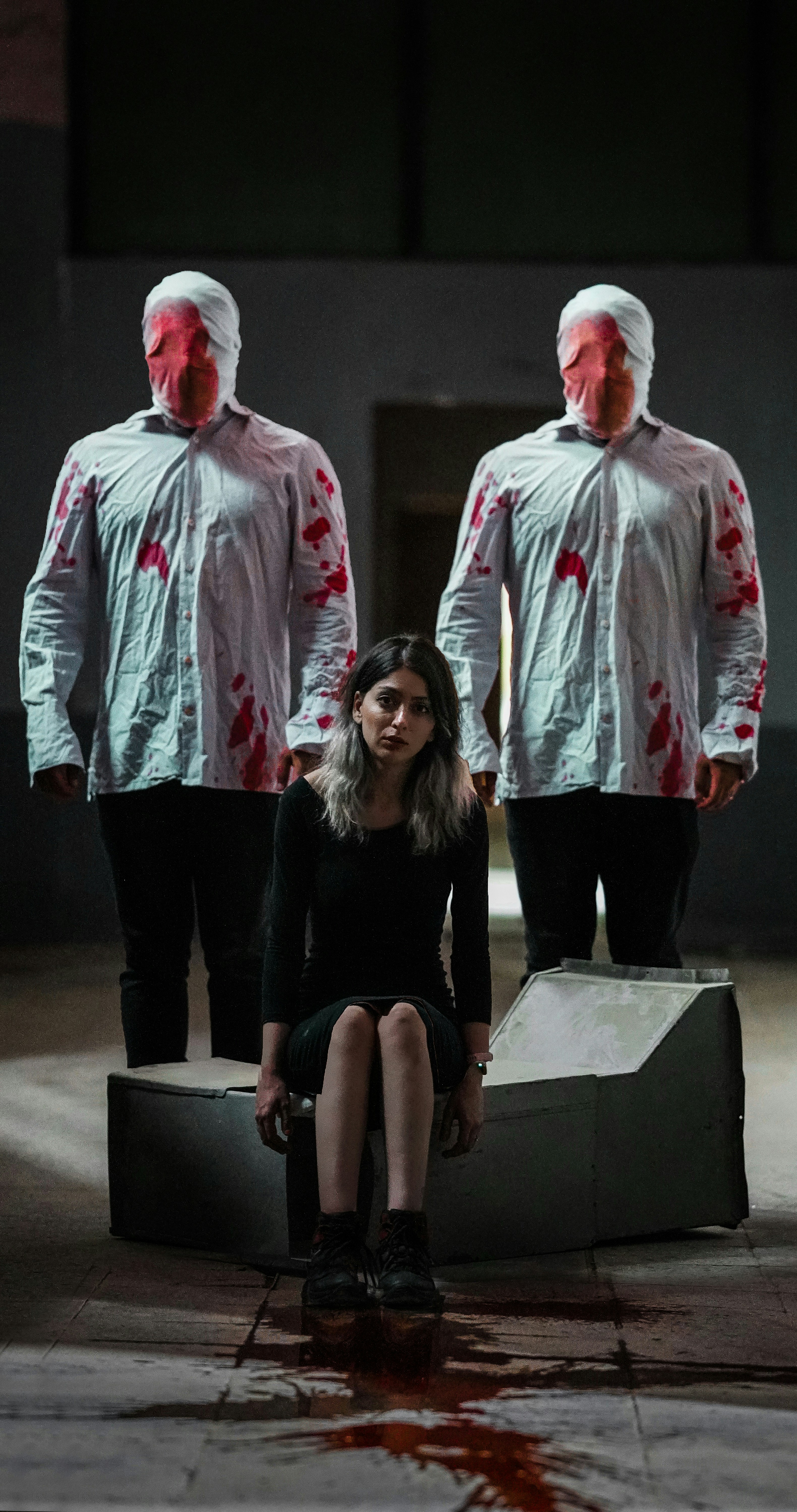 Center Stage in the Dark: A Seated Woman Between Hooded Hazmat Figures