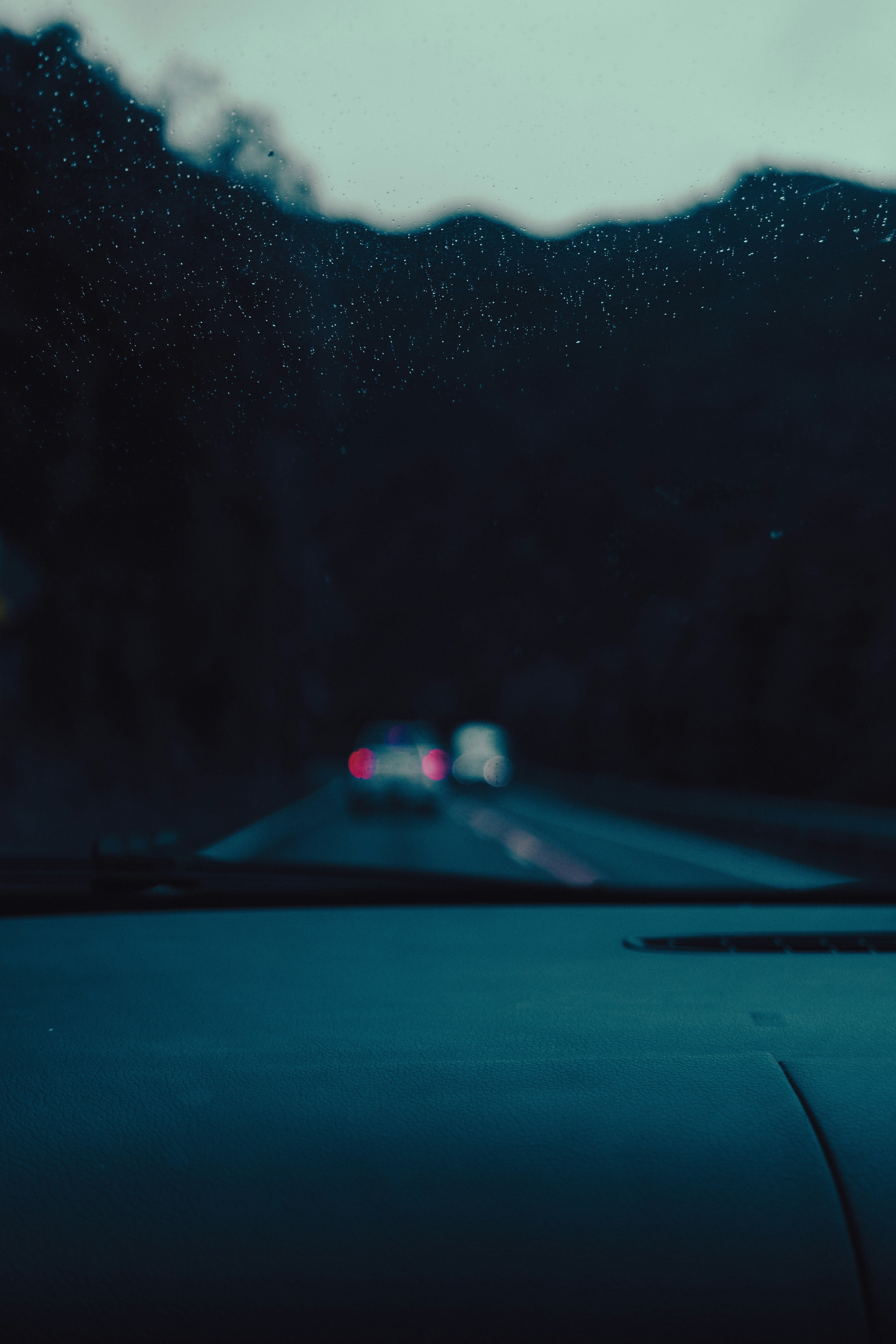 View from inside a car capturing rain droplets on the windshield with blurred headlights of vehicles ahead on a winding road.