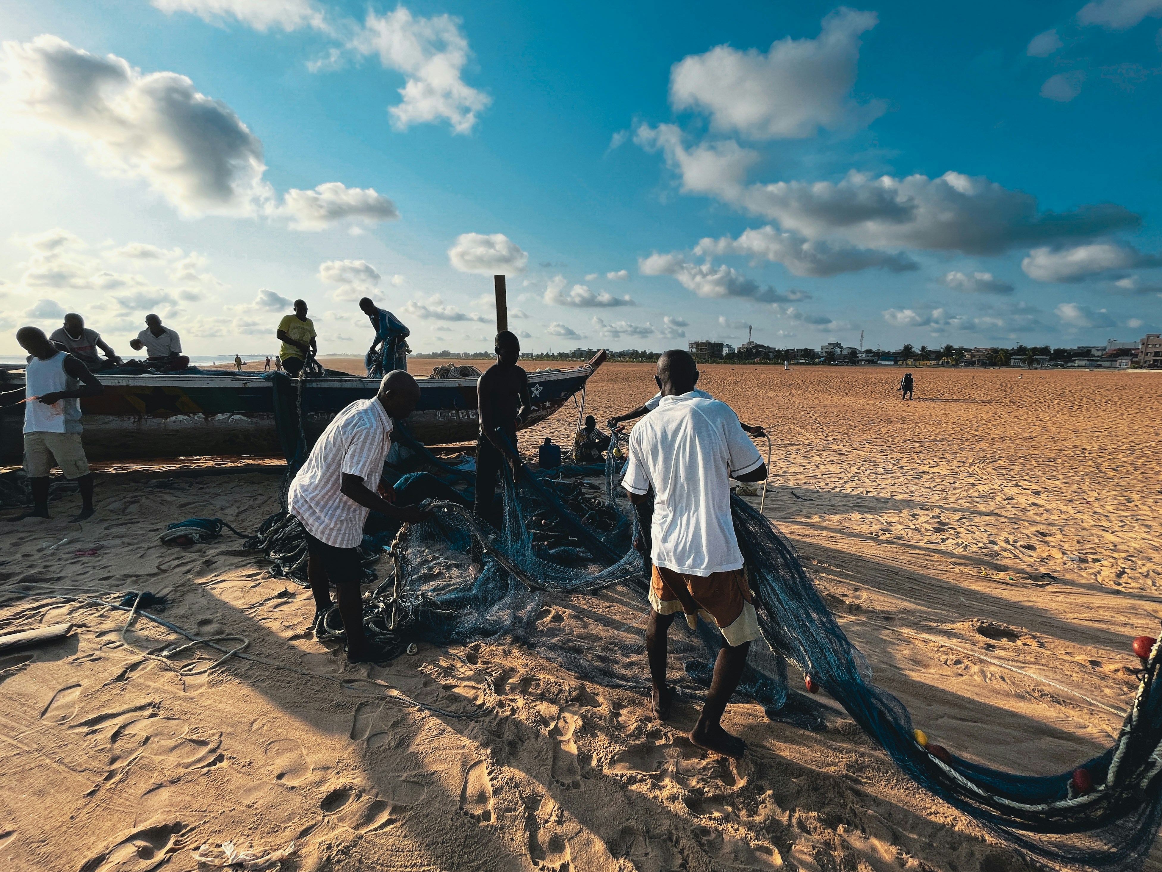 Les pêcheurs de la plage de Fidjrossè au Dahomey actuel Bénin. | a group of men working on a boat on the beach