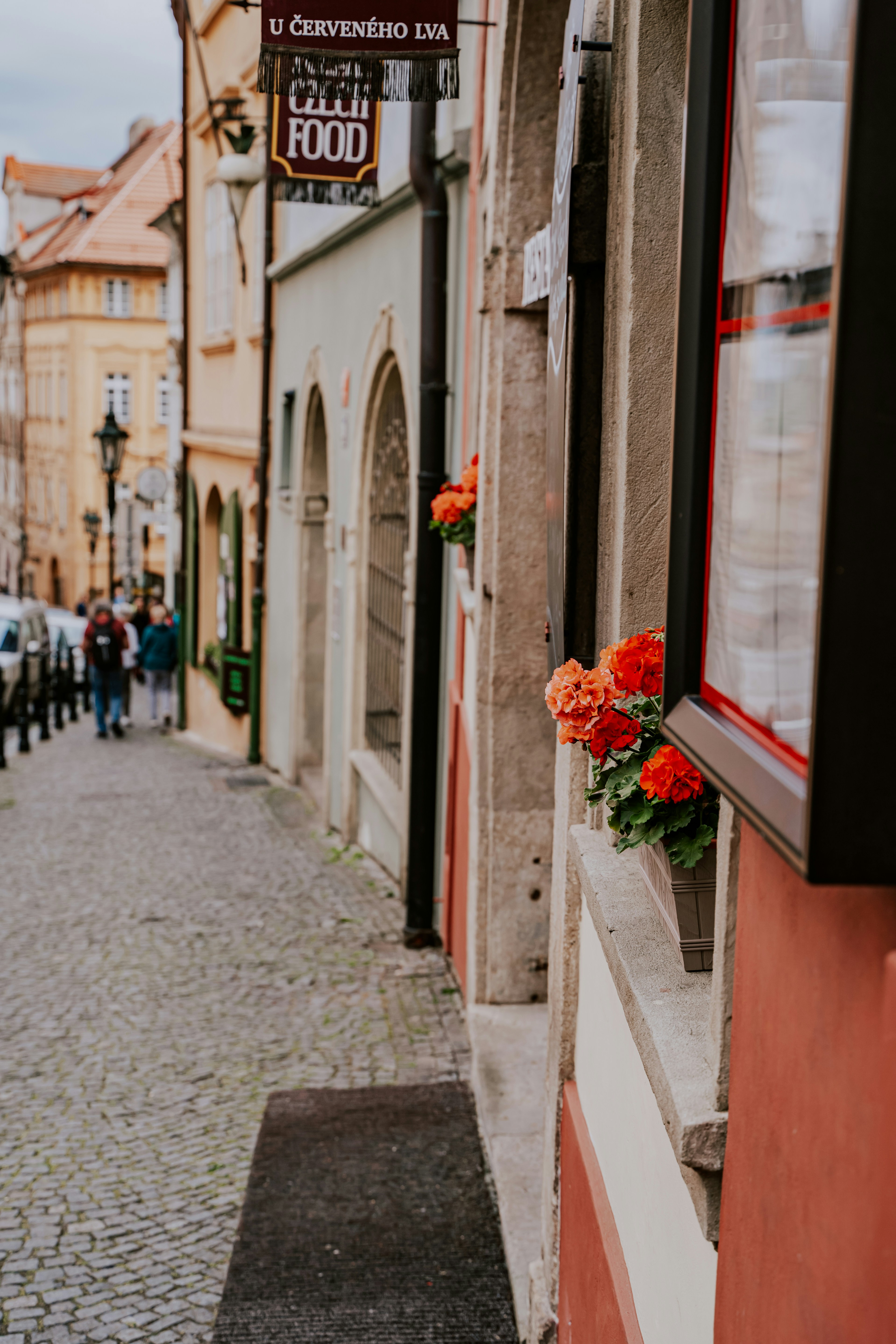 Quaint cobblestone street lined with colorful flower boxes and vintage signage, inviting passersby to explore local eateries.