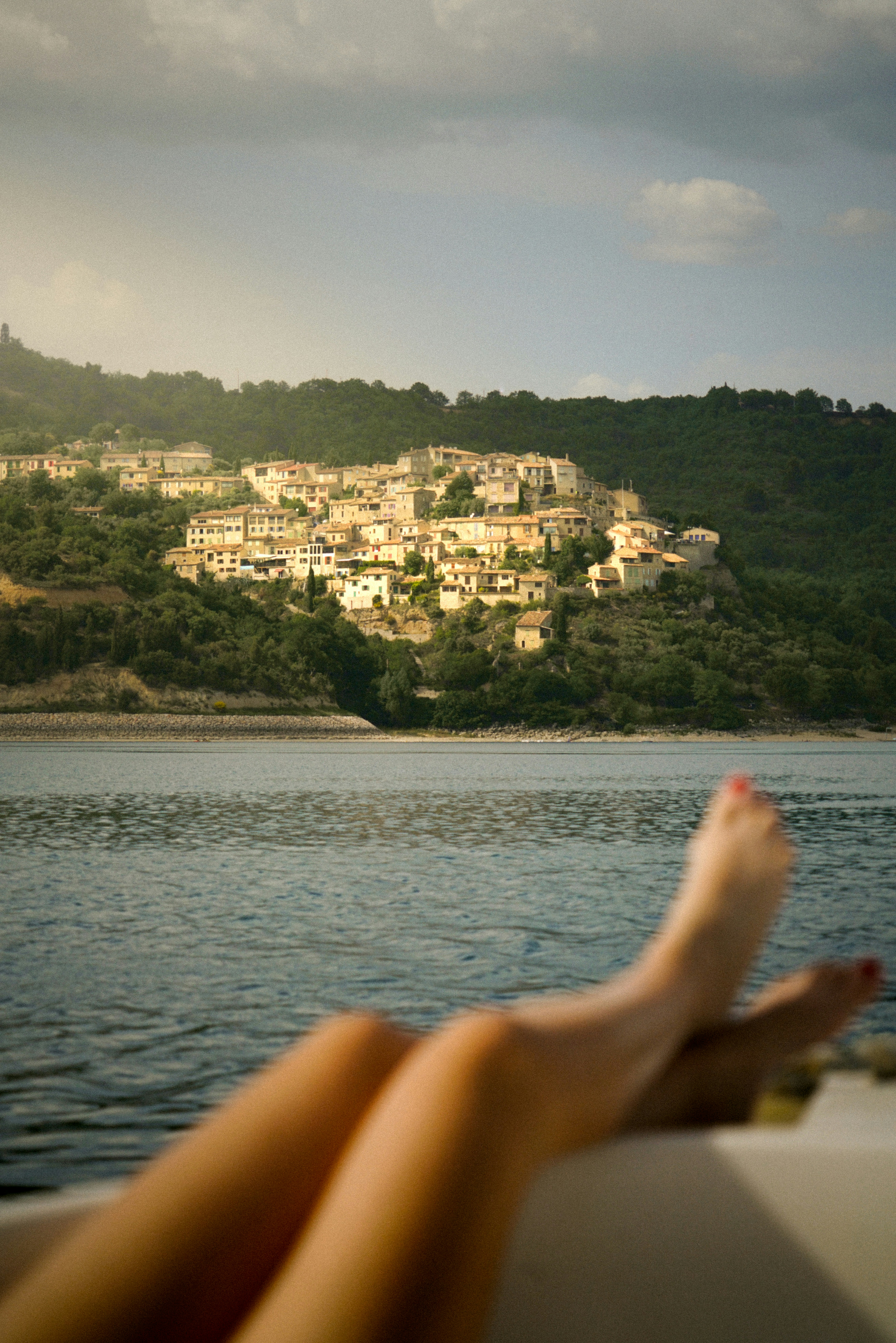 Sunlit hillside village rising above a calm bay, viewed from a languid boat