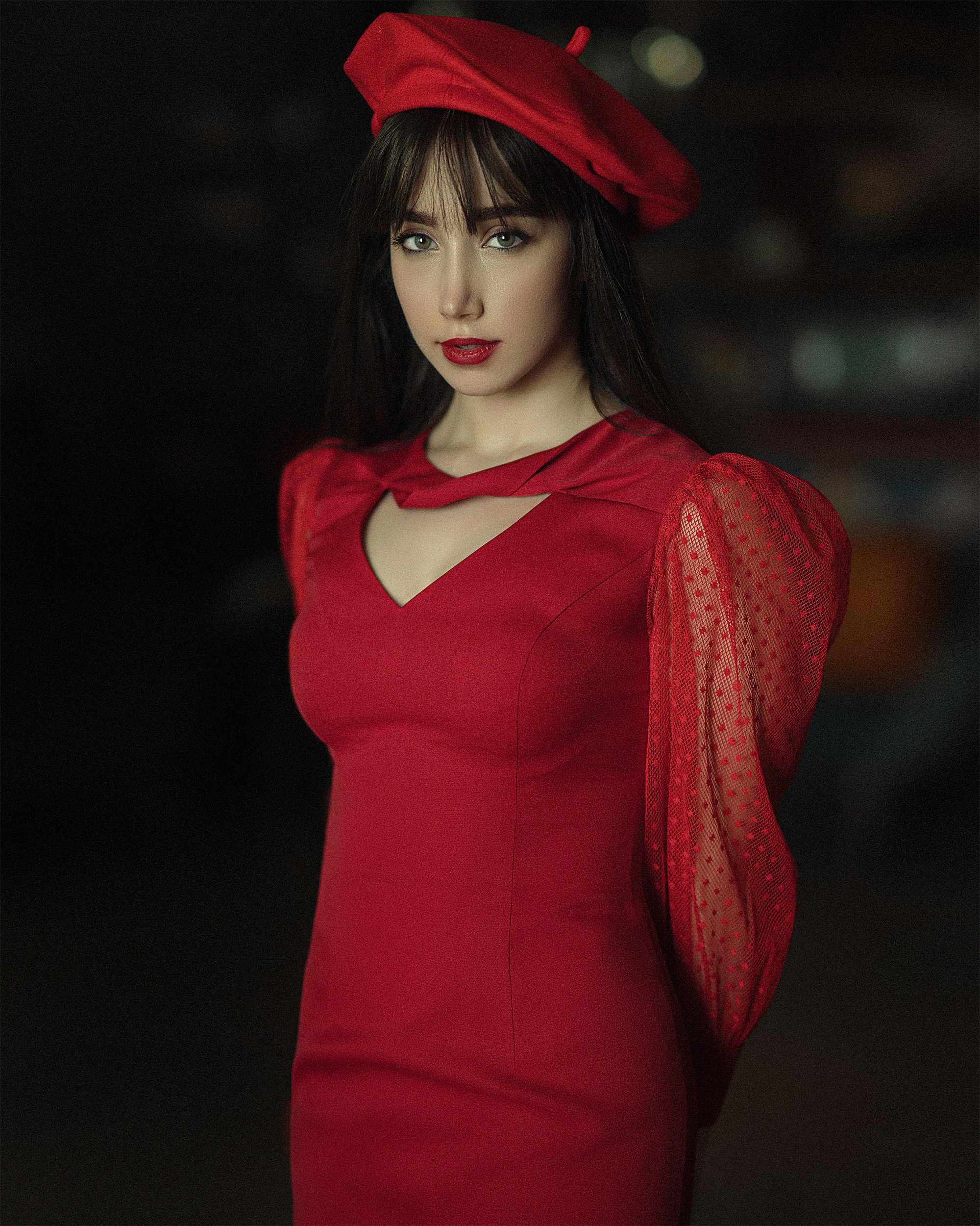 Model in a striking red dress and beret poses against a softly blurred background, showcasing a blend of contemporary fashion and classic charm.