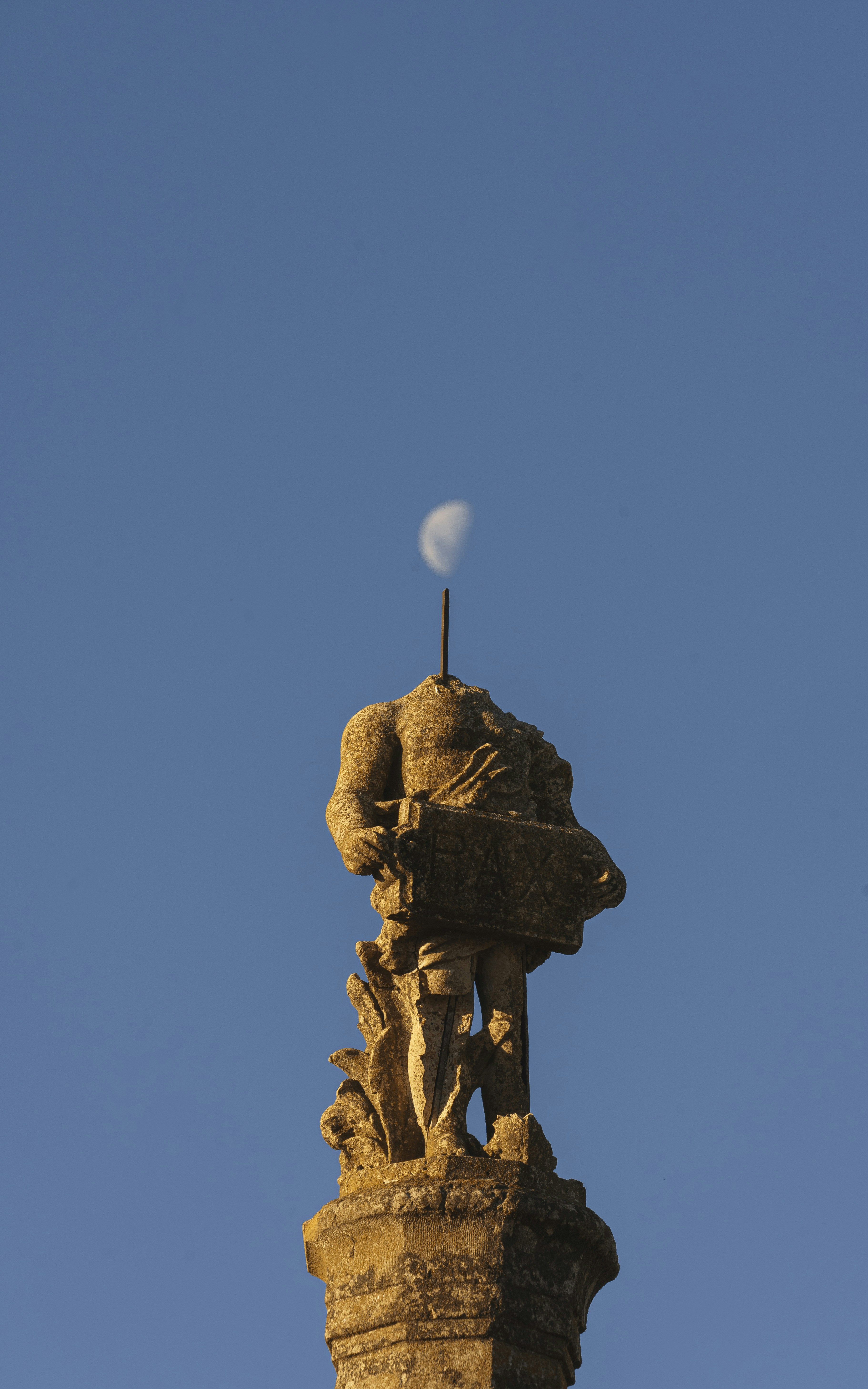 Moonbound Sentinel: A Weathered Statue Against a Cerulean Sky