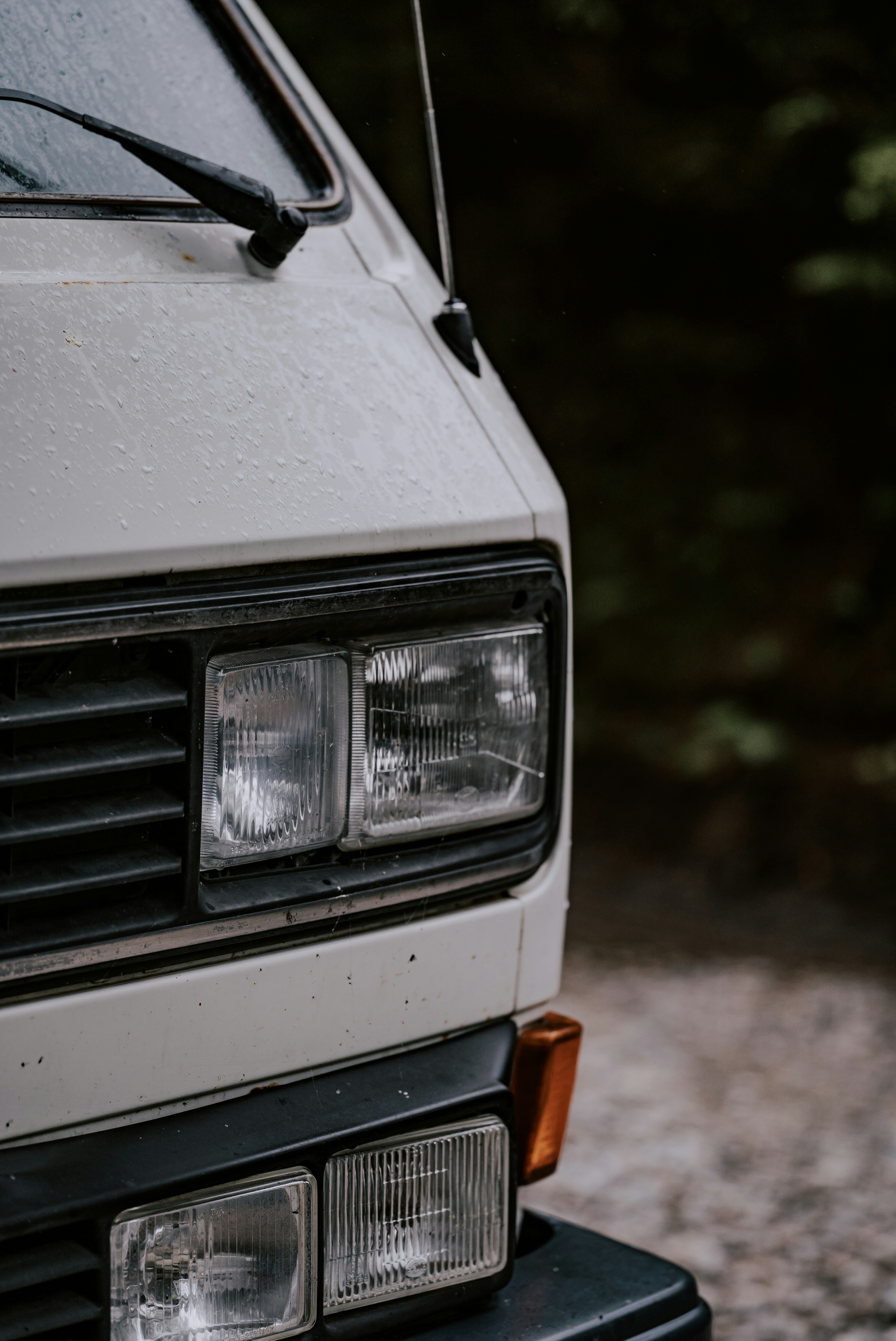 Close-up of a vintage van's front, showcasing its headlights and grill, accentuated by raindrops. The scene evokes a sense of adventure and nostalgia.