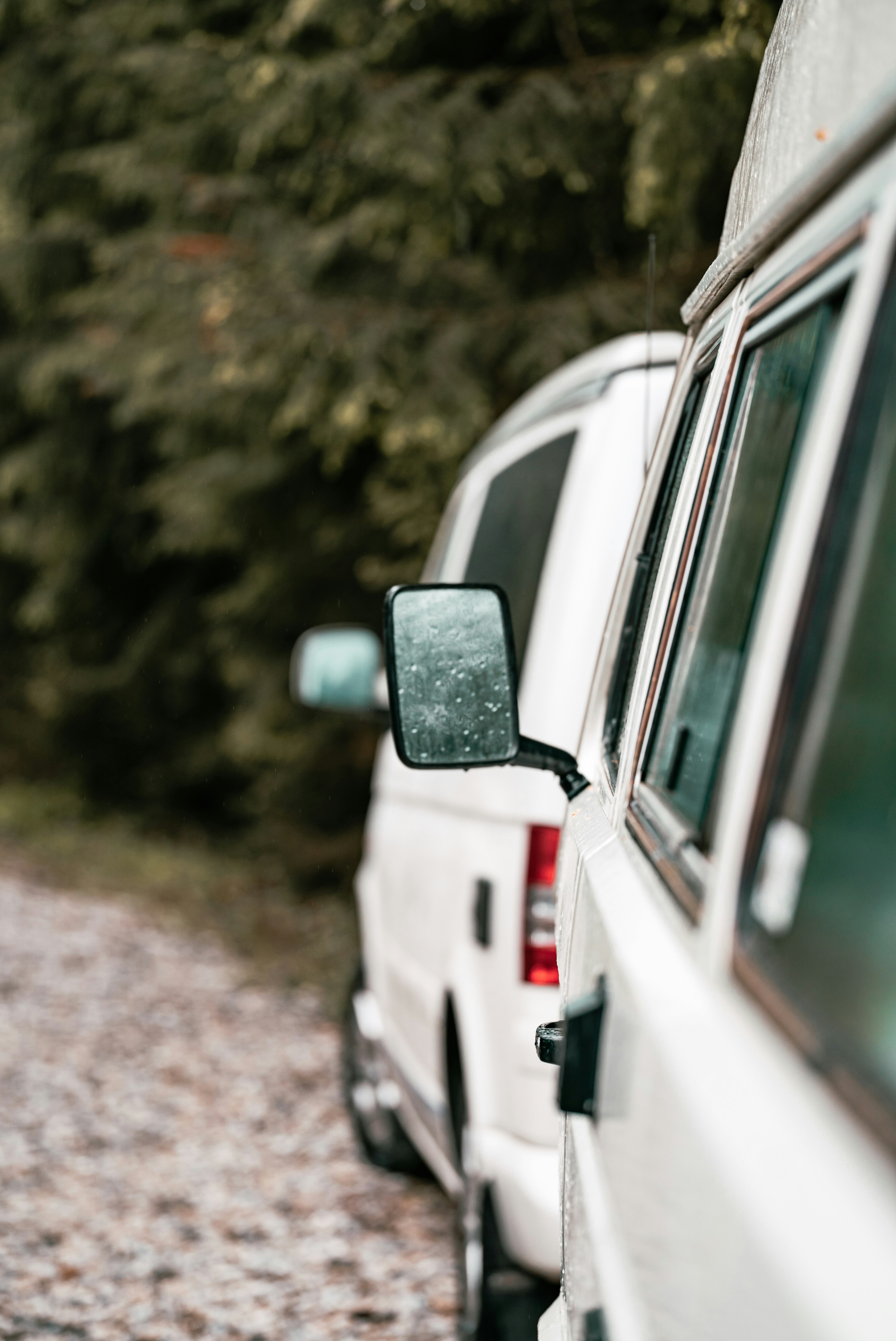 Close-up of a vintage camper van's side mirror, capturing raindrops and the blurred silhouette of another vehicle nearby.