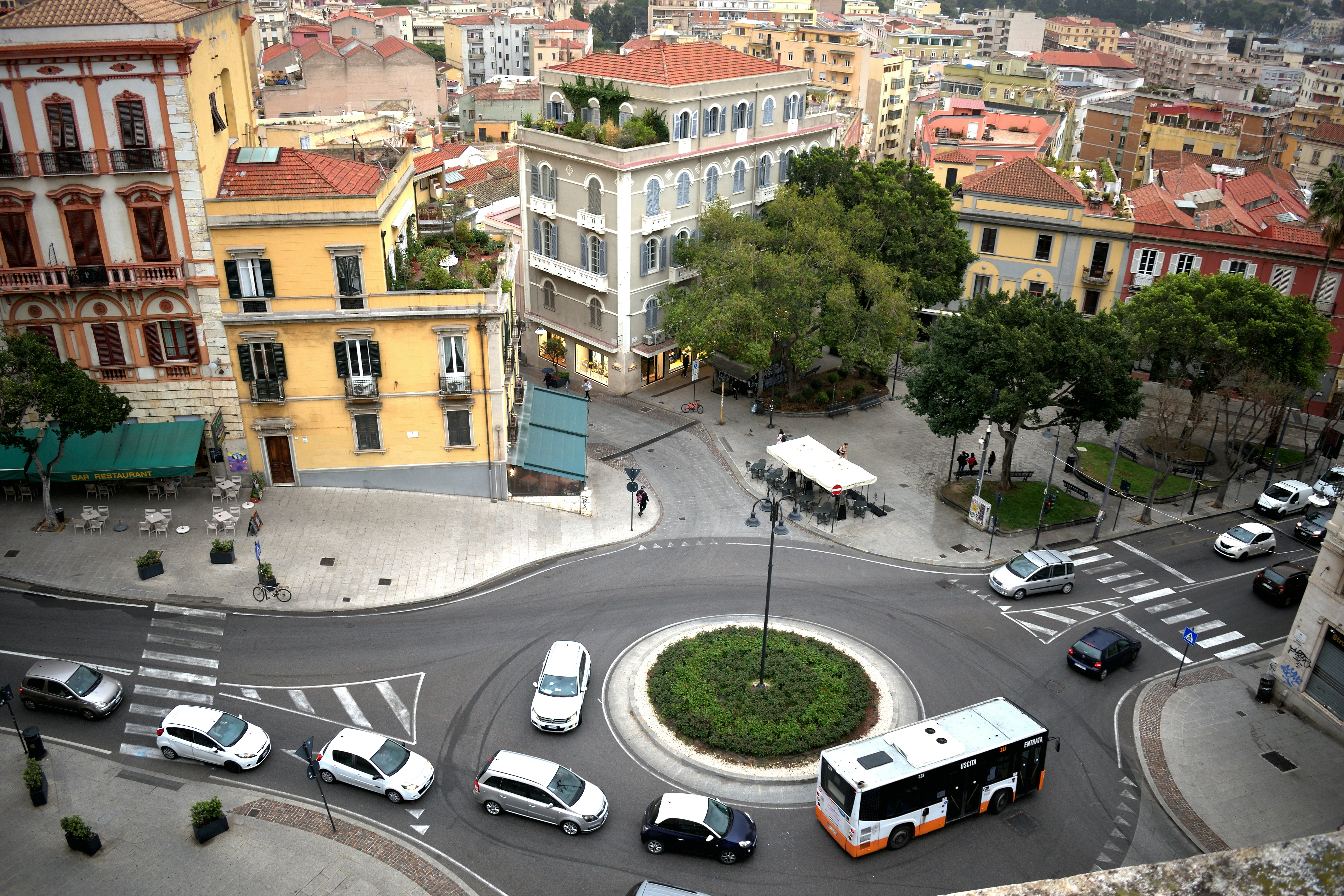 Roundabout in Cagliari surrounded by historic buildings and a bus navigating through traffic.
