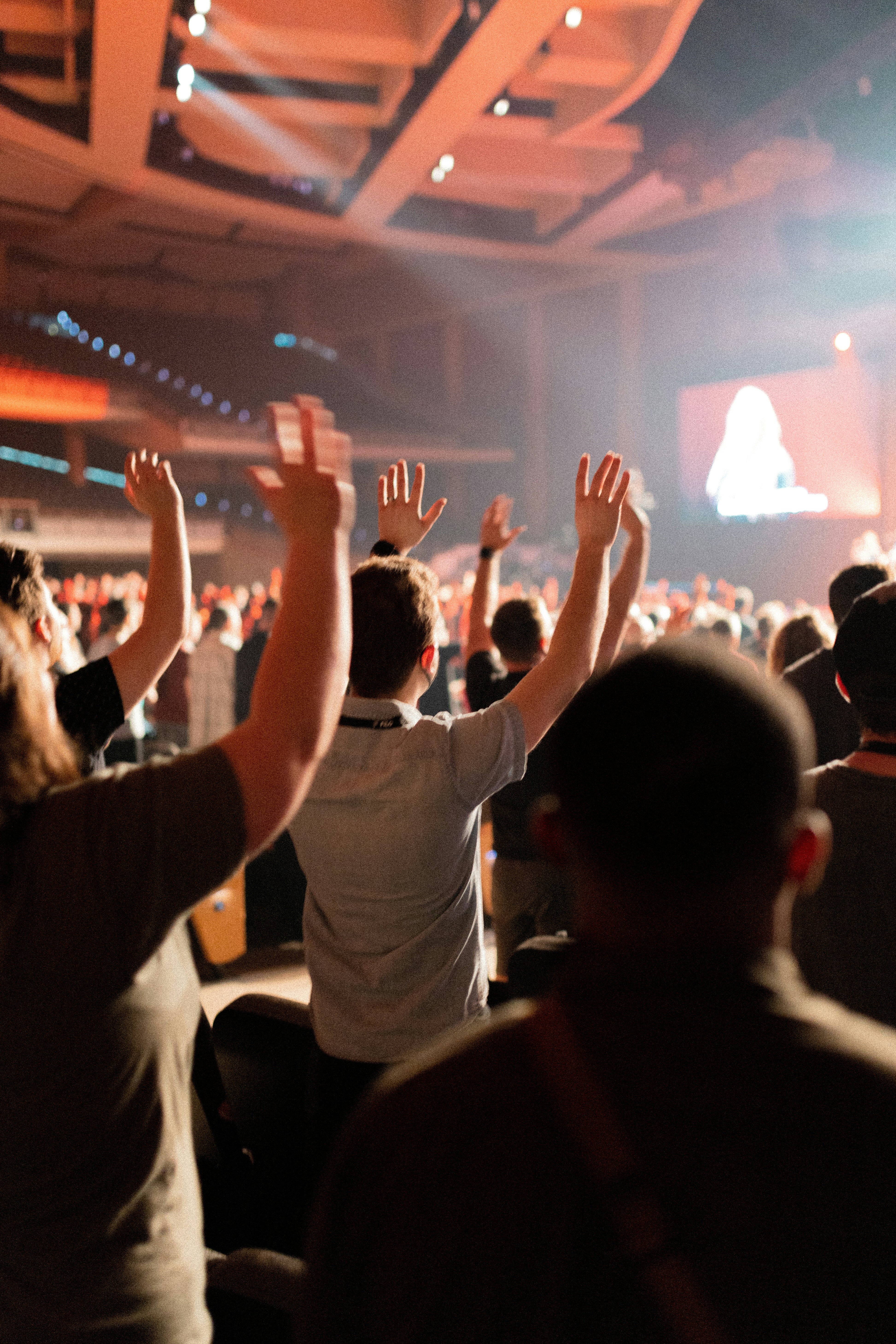 Audience with hands raised in a moment of collective engagement during an event. The atmosphere is filled with energy and connection.