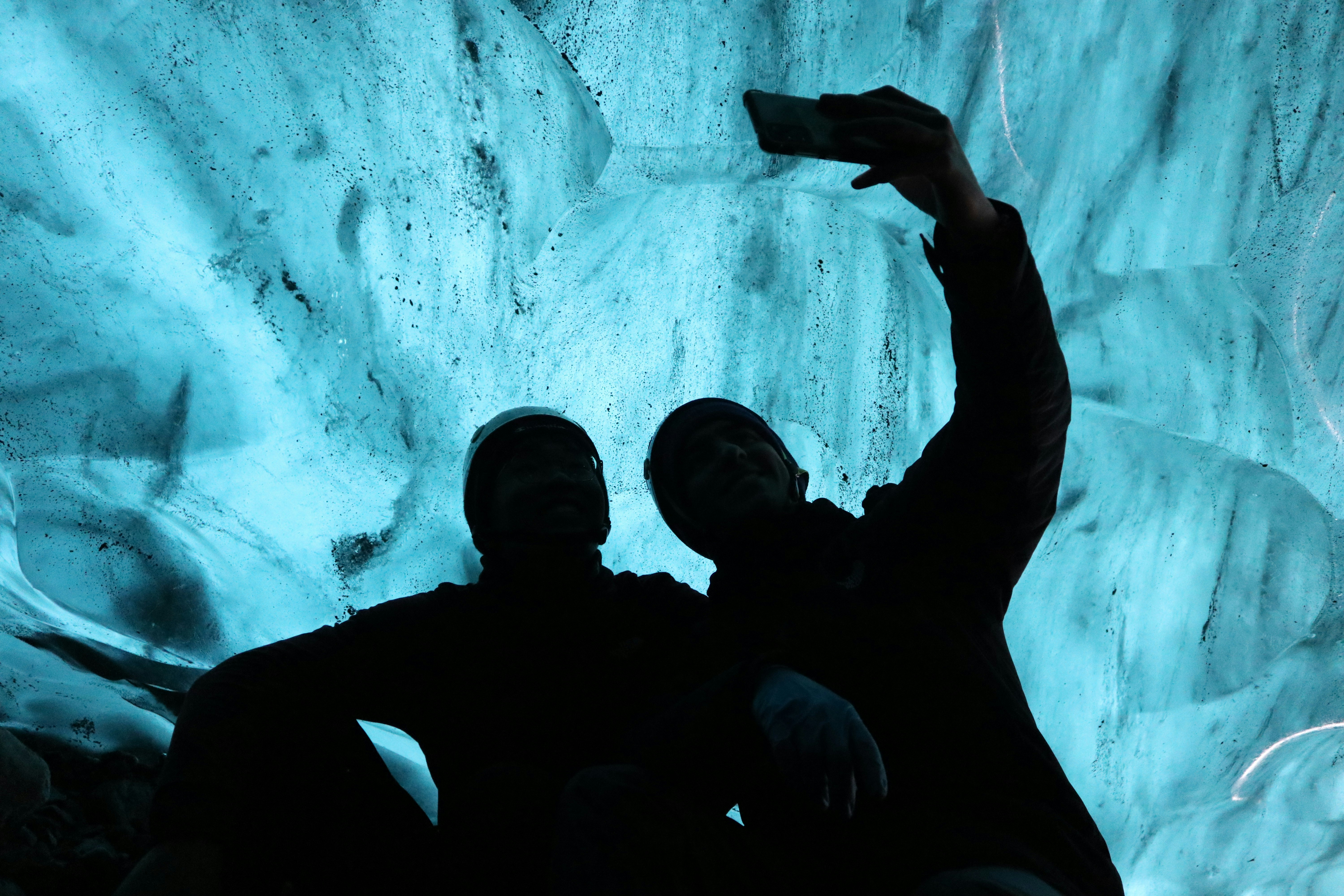 Cobalt Glacier Selfie: Two silhouettes frame a glowing blue ice cavern