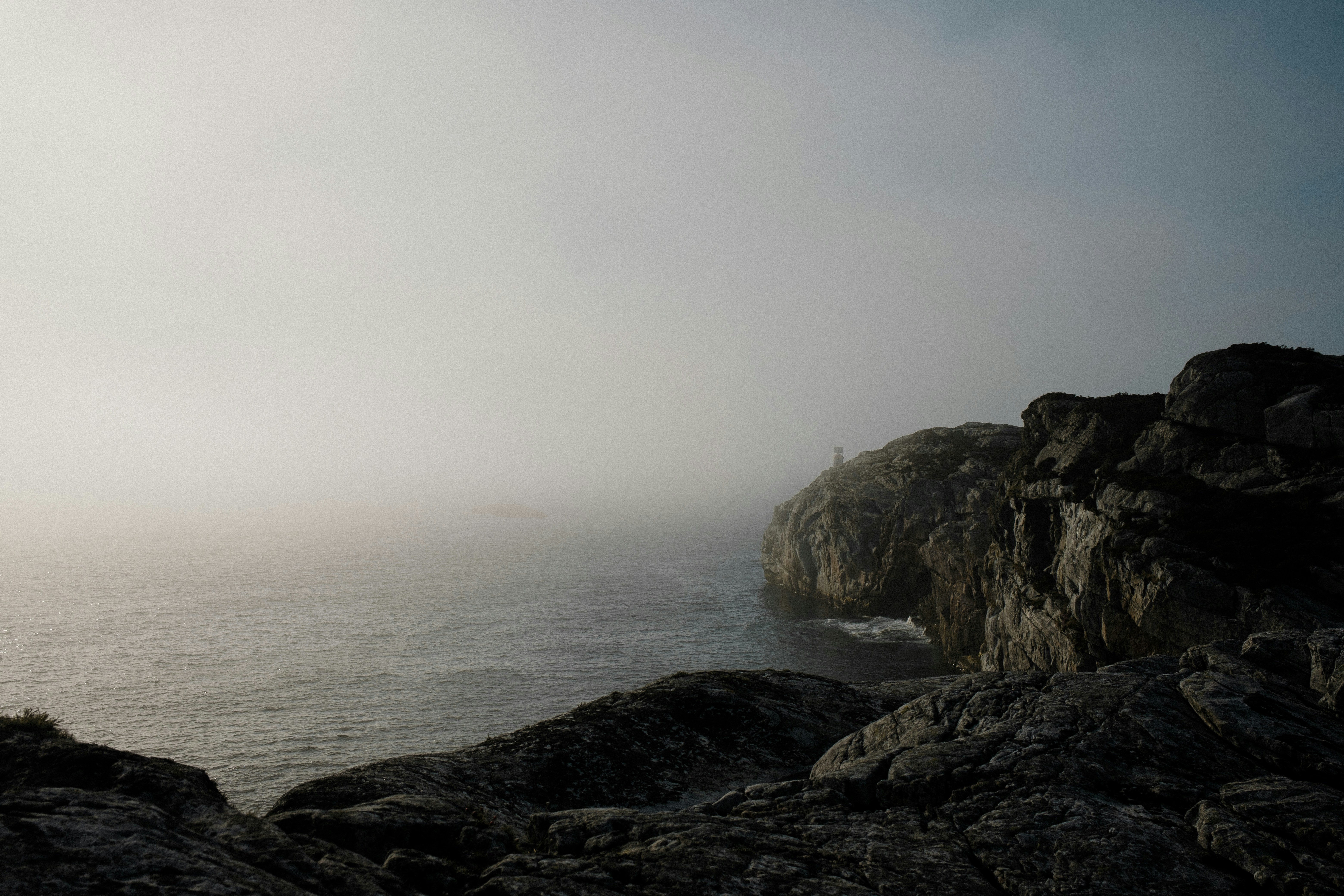 Rocky cliffs meet a fog-covered sea under a muted sky.