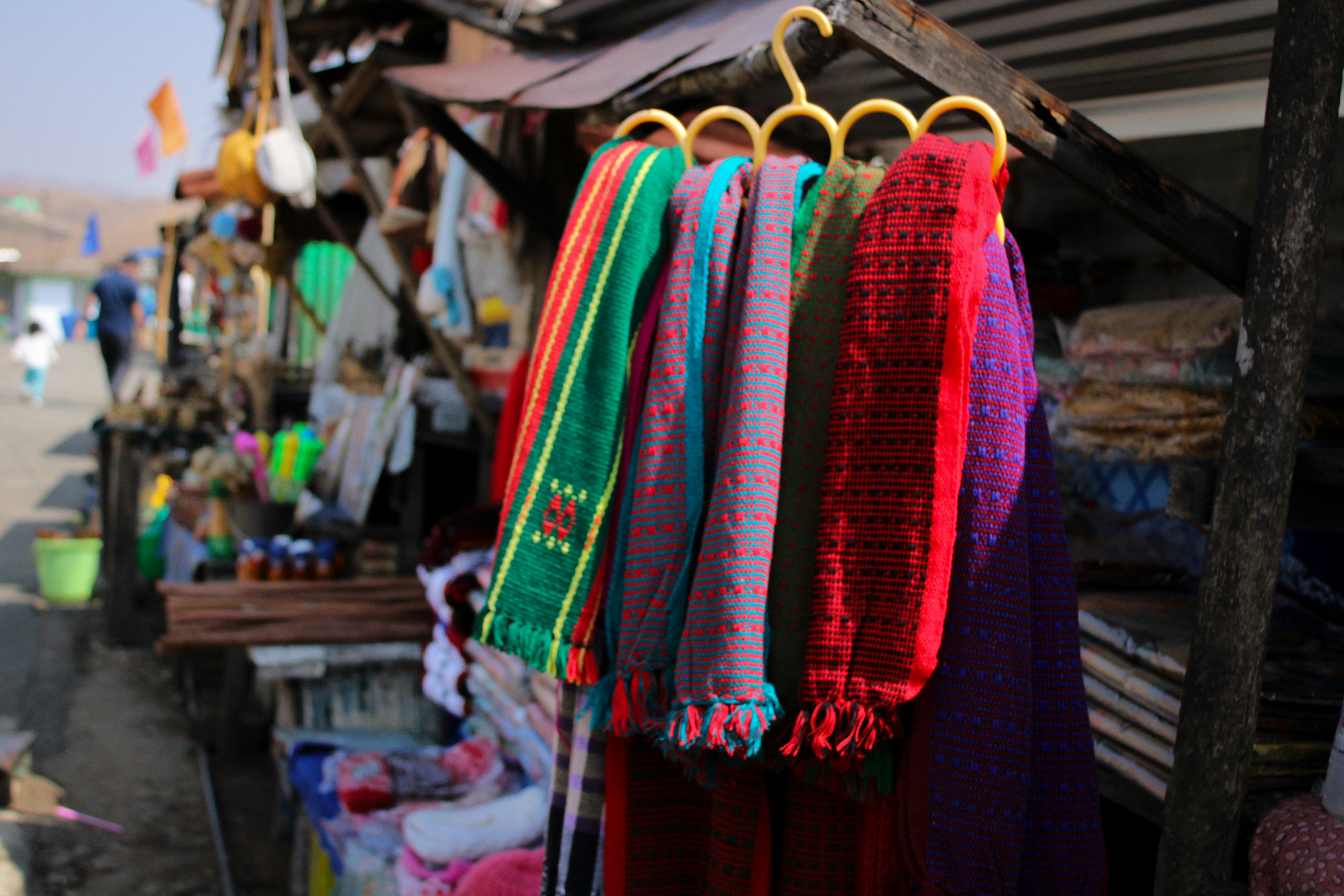 Colorful scarves hanging on wooden racks in an outdoor market stall.