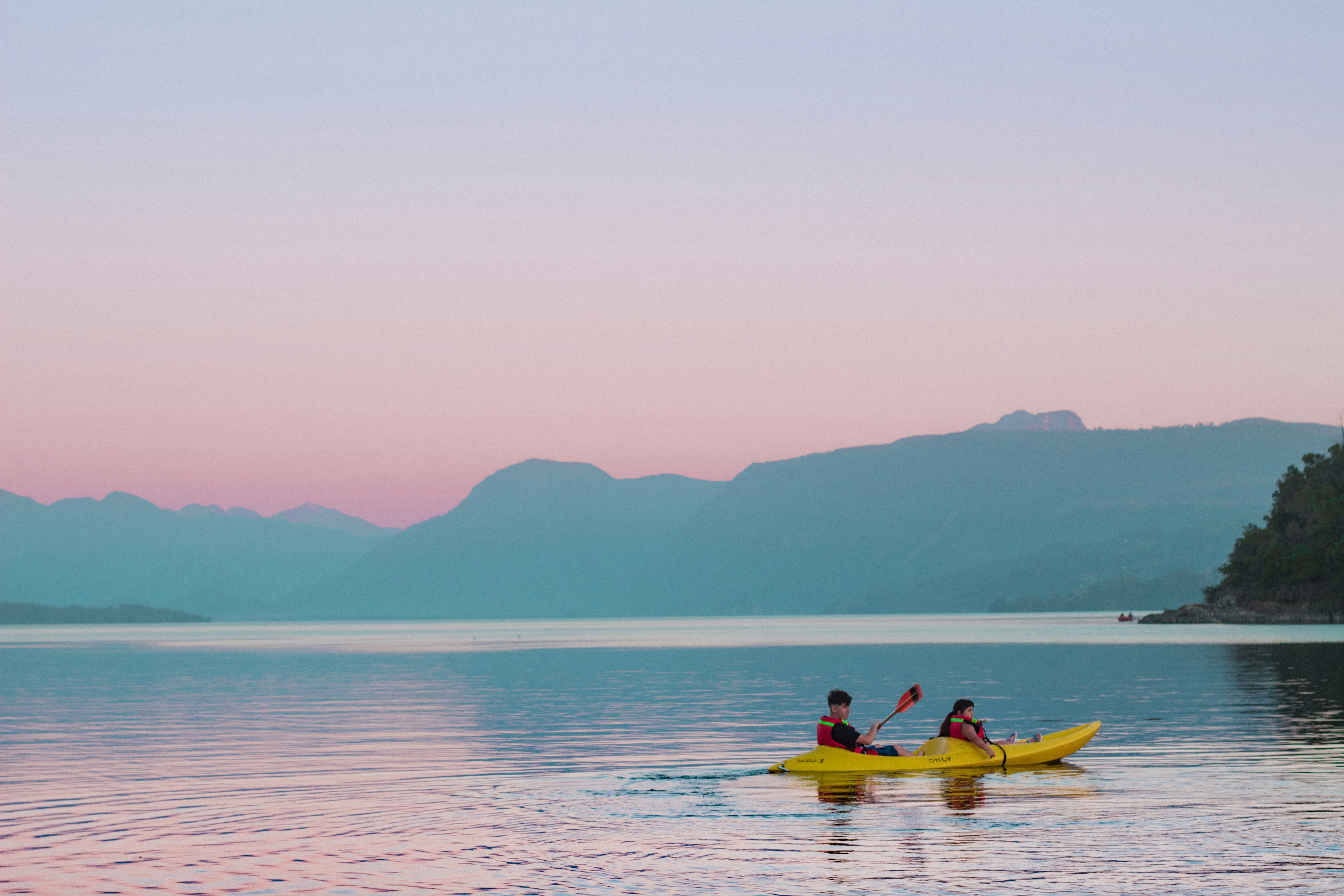 Two people paddle a yellow kayak across a tranquil lake under a pastel twilight sky.