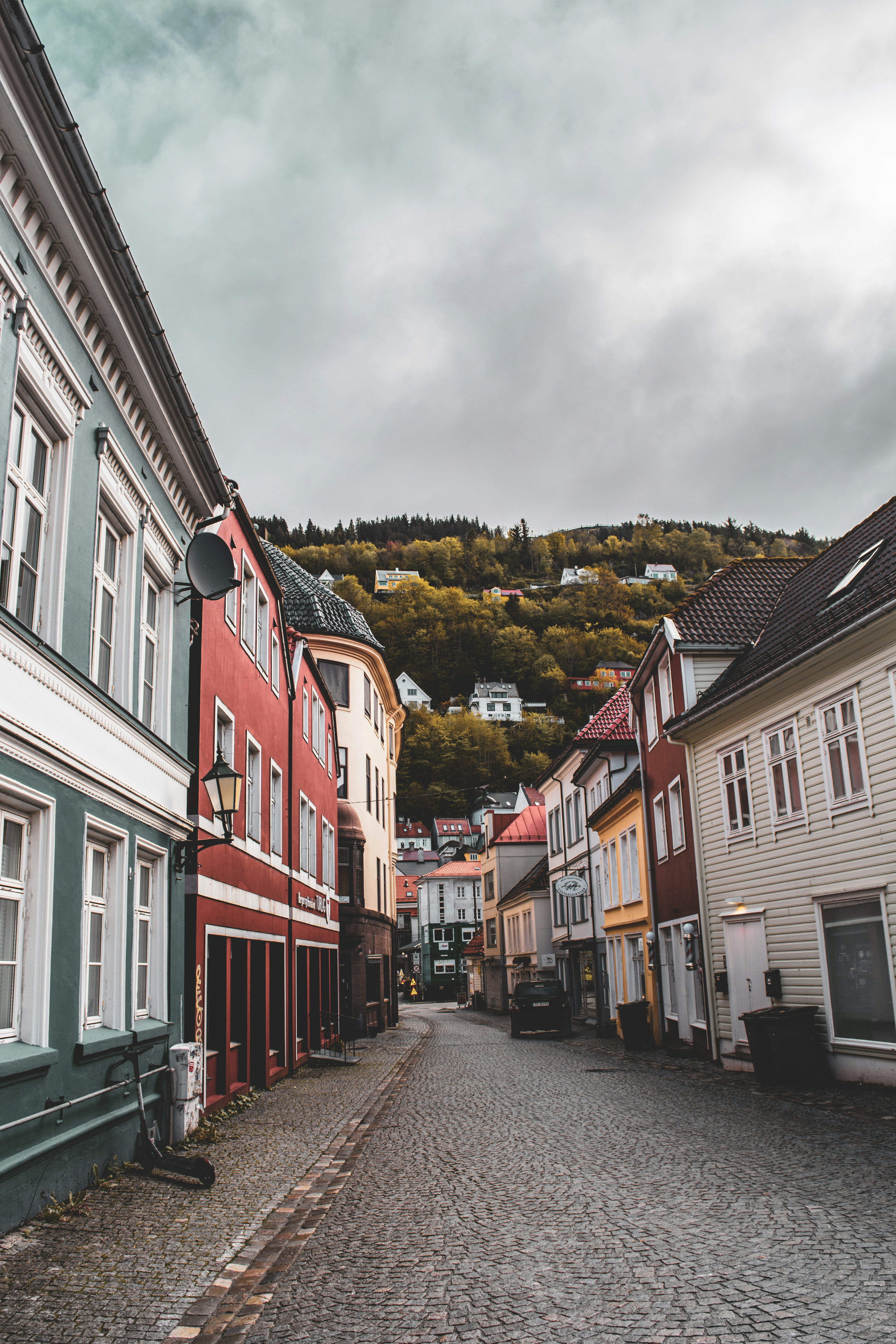 Narrow cobblestone street lined with colorful houses leading towards a hillside in Bergen, Norway. The scene captures the quaint essence of the town.