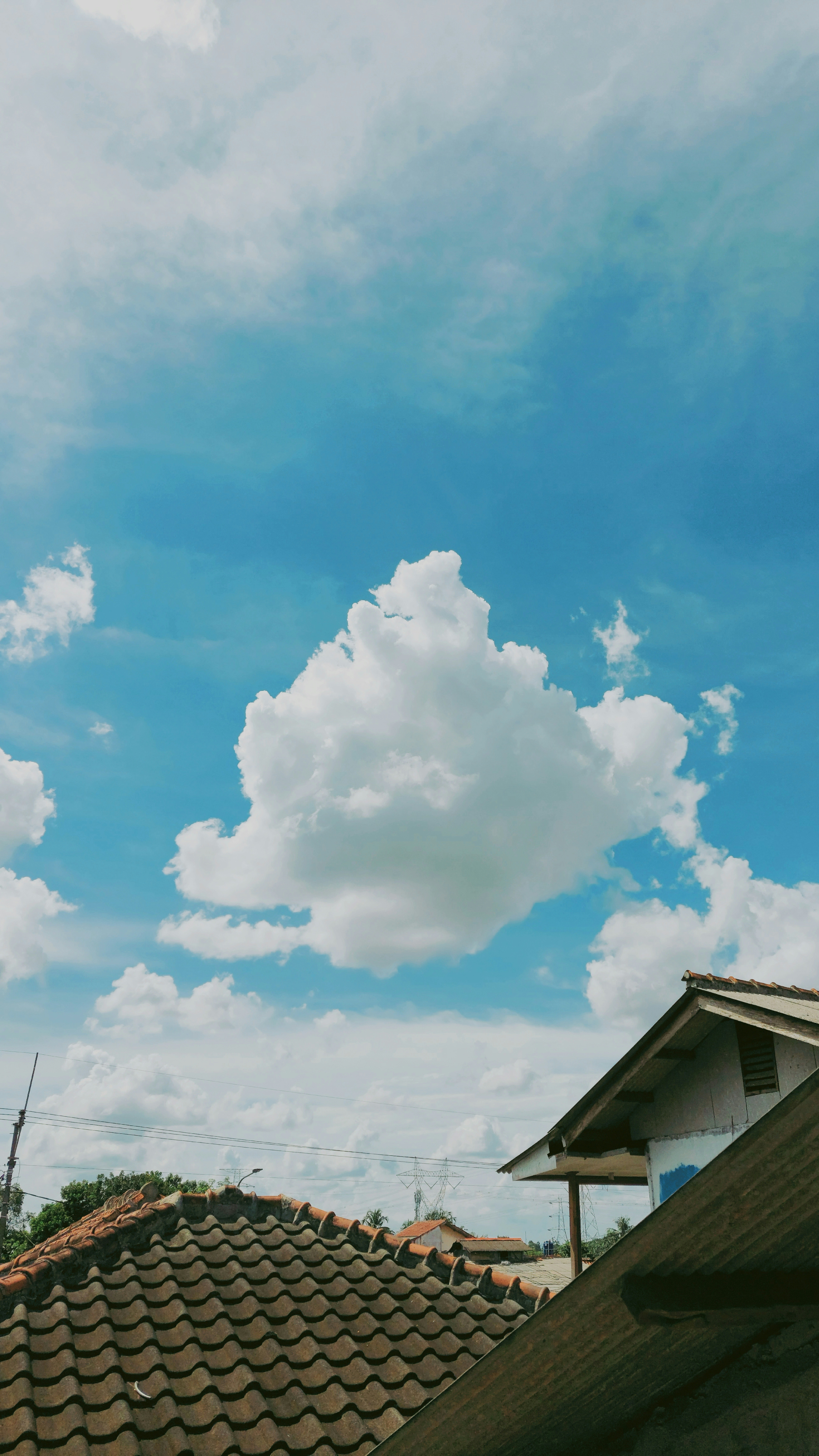 Fluffy white clouds drift across a bright blue sky, framed by terracotta rooftops and distant greenery. A tranquil scene capturing the essence of a peaceful day.