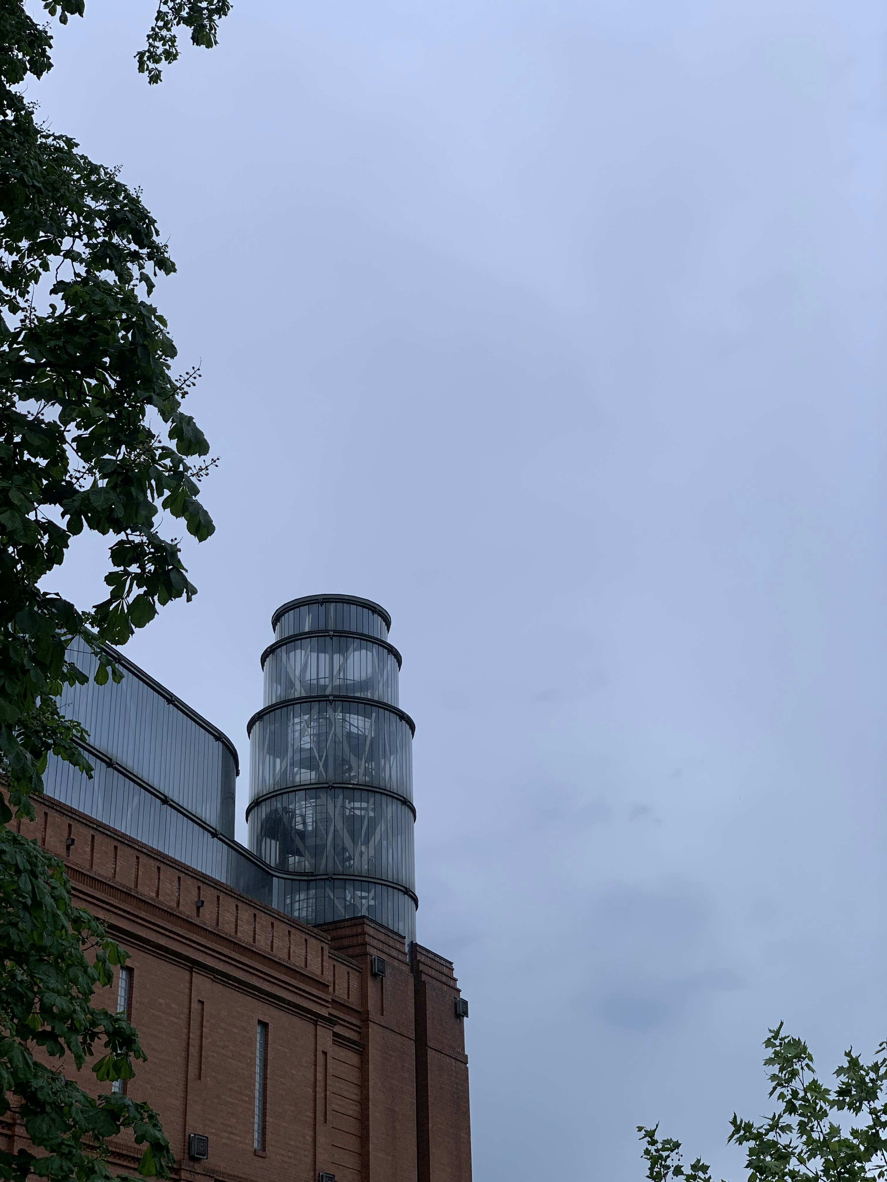 Cylindrical Glass Turret Rising from a Brick Facade Under a Calm Sky
