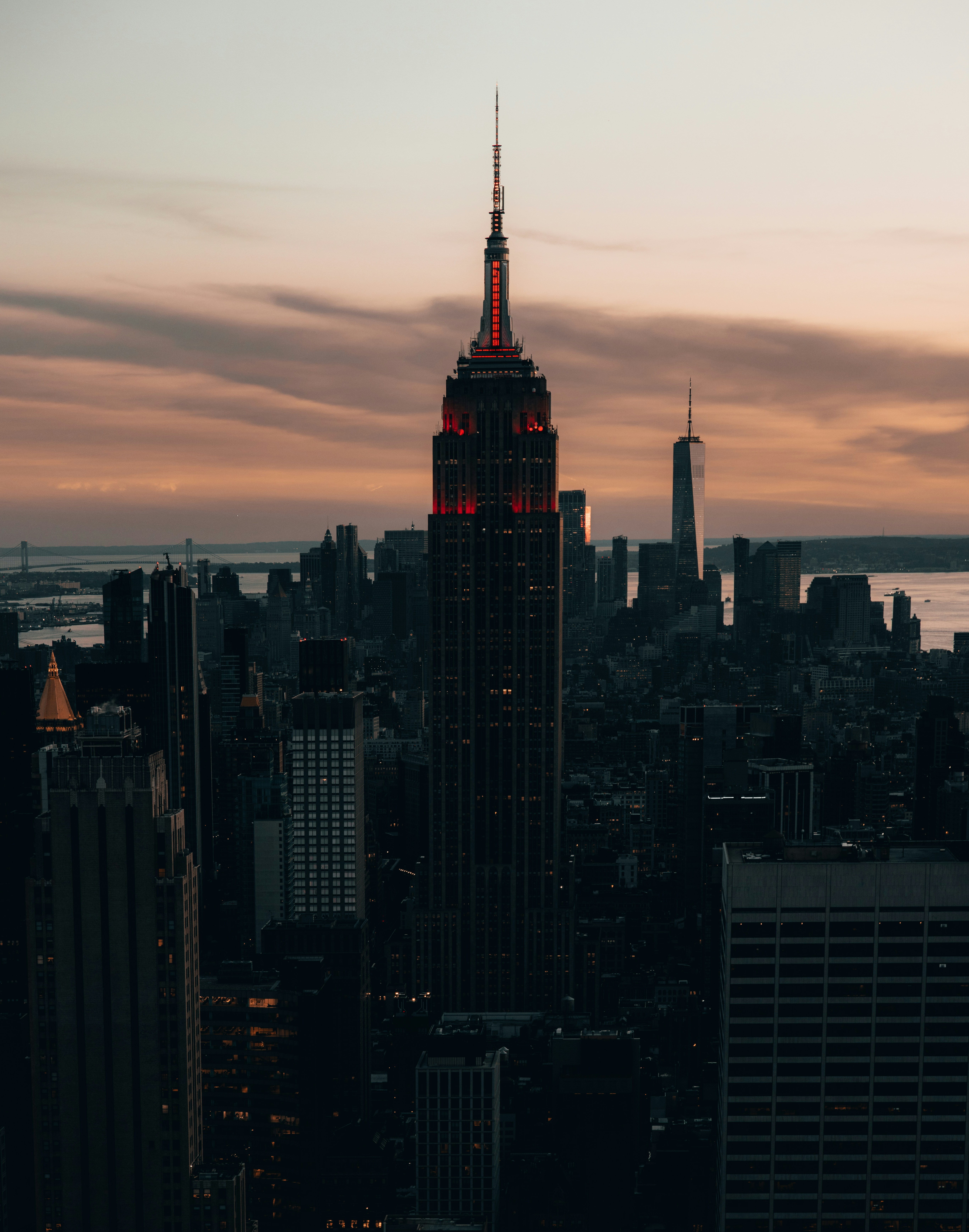 Empire State Building illuminated in red against a twilight skyline, showcasing the city’s architectural grandeur. The horizon glows softly with the fading light.