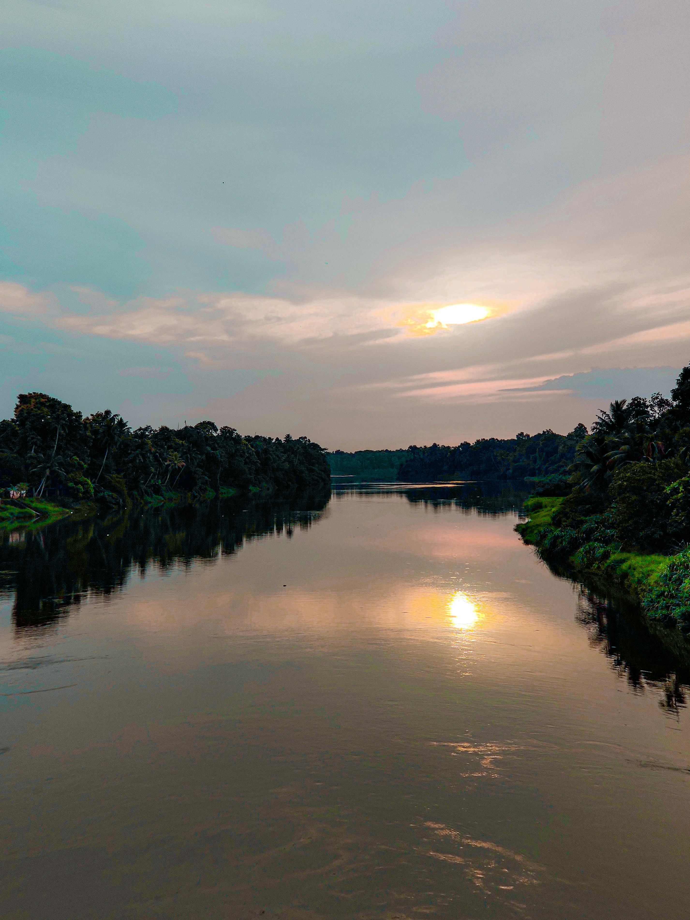 Sunset over a calm river with lush greenery and trees lining the banks.