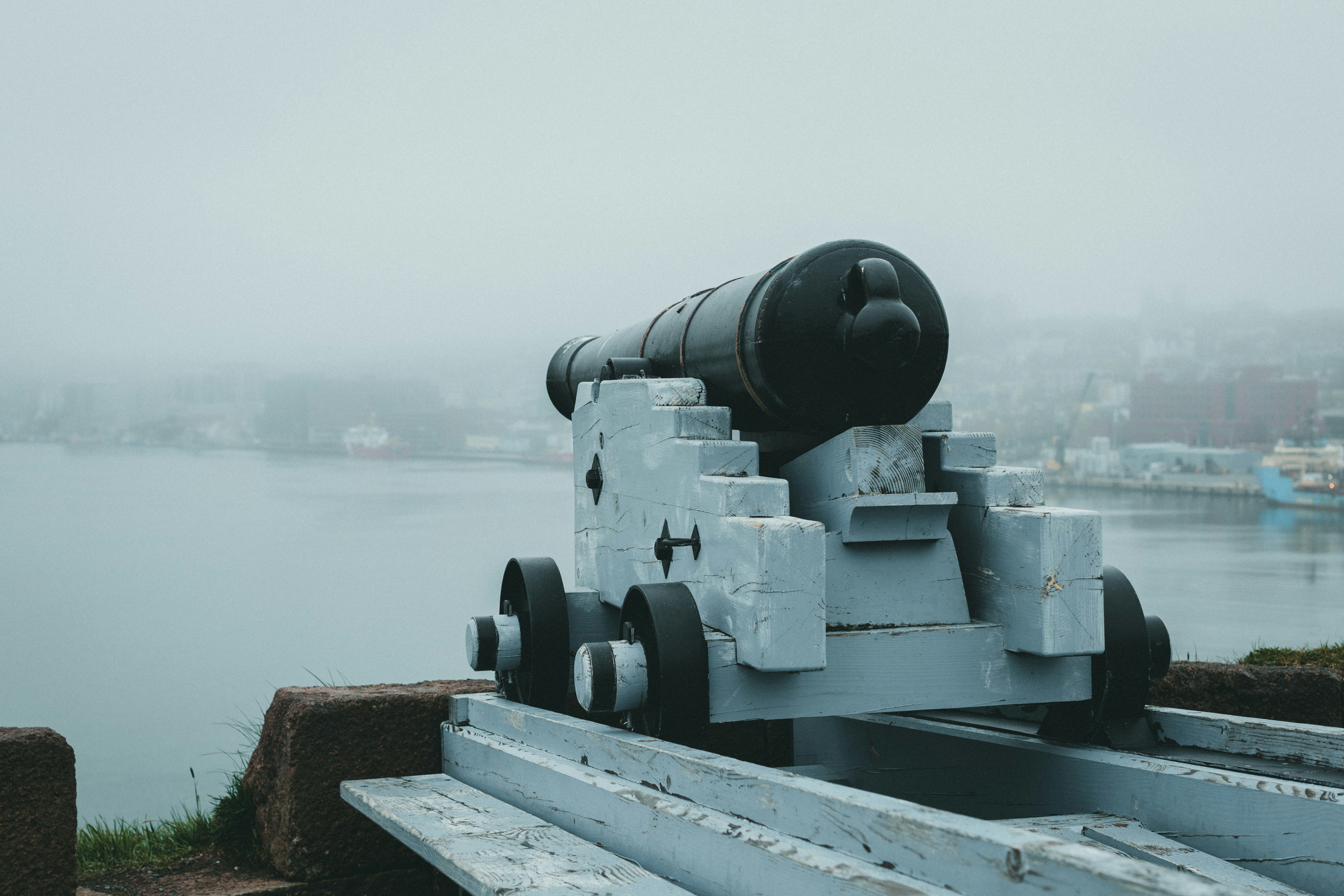 Historic cannon positioned on a stone platform overlooking a foggy harbor, emphasizing maritime heritage.