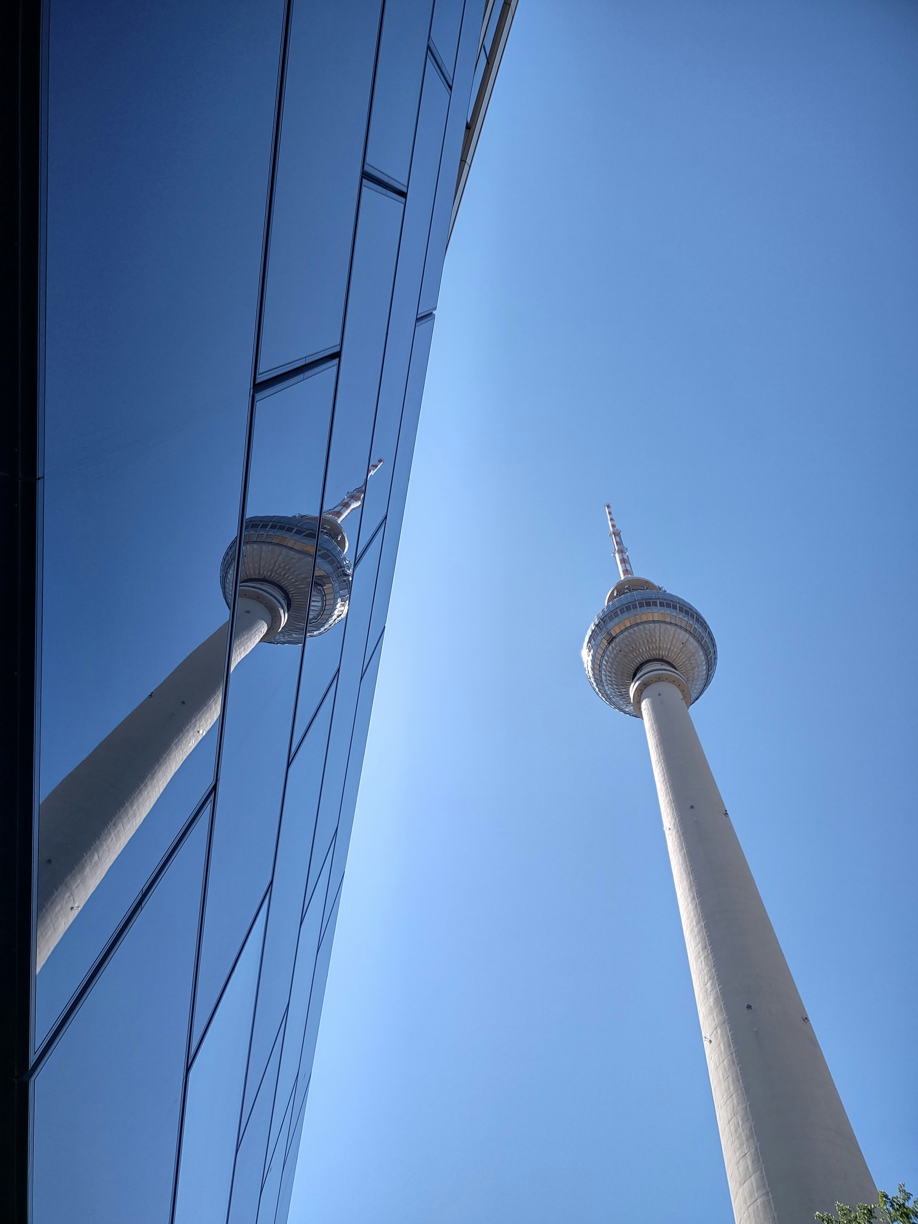 Vertical Towers, Blue Sky: A Ground-Low View of Berlin’s TV Spire and Modern Facade