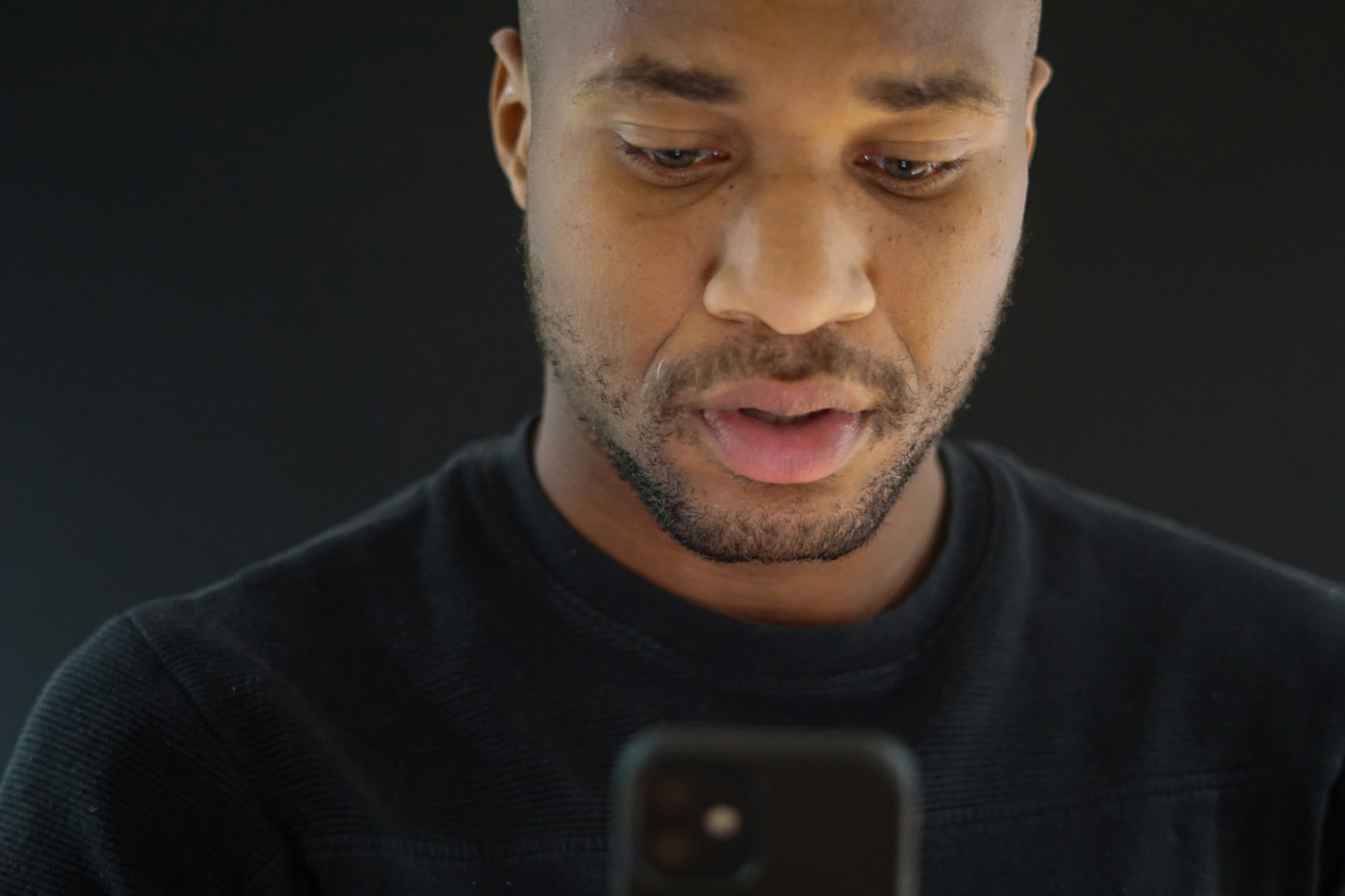 Man focused on his smartphone, illuminated by soft light against a dark background.