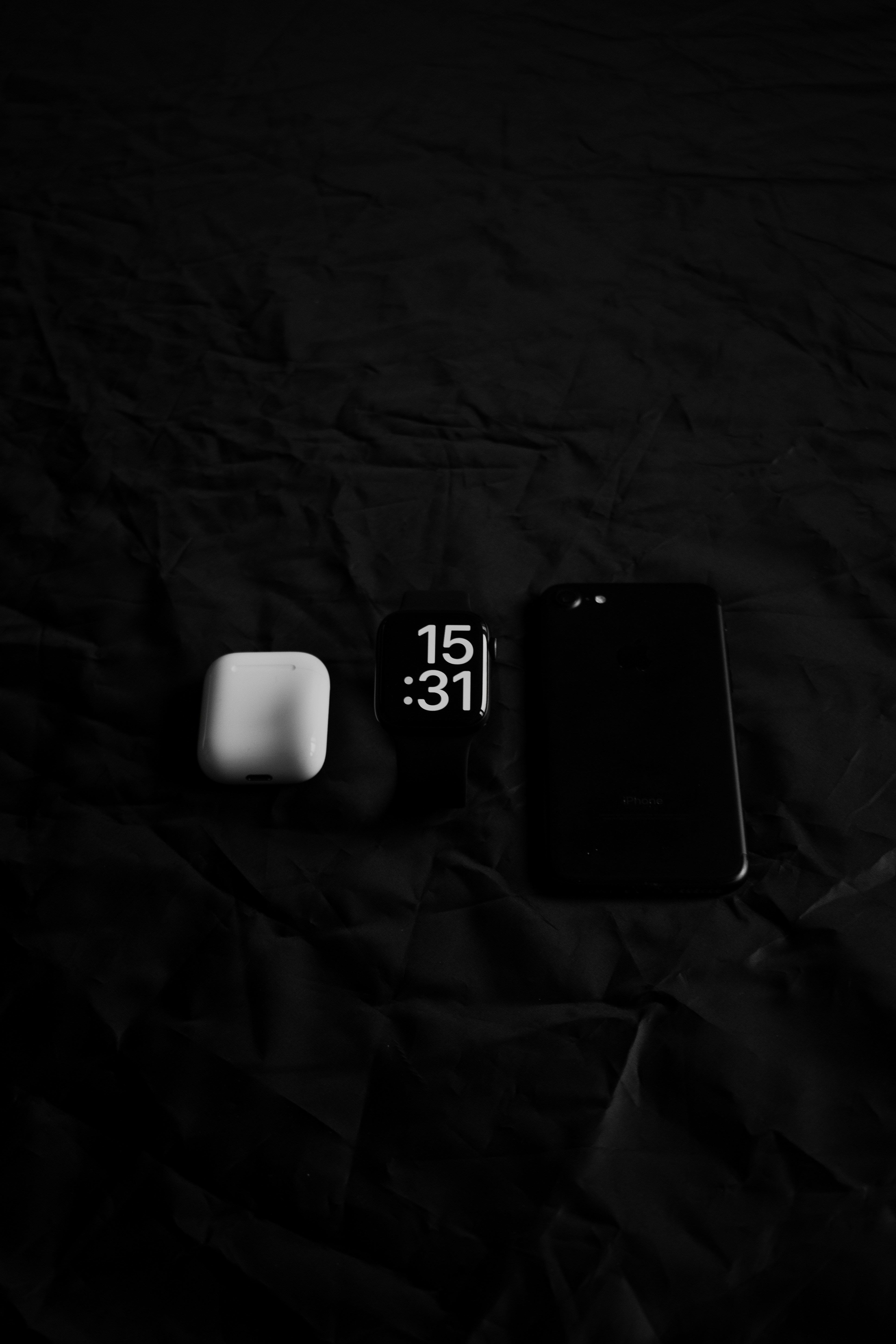 Nocturne Trio on Dark Fabric: White AirPods, Time Tile, and a Sleek Phone