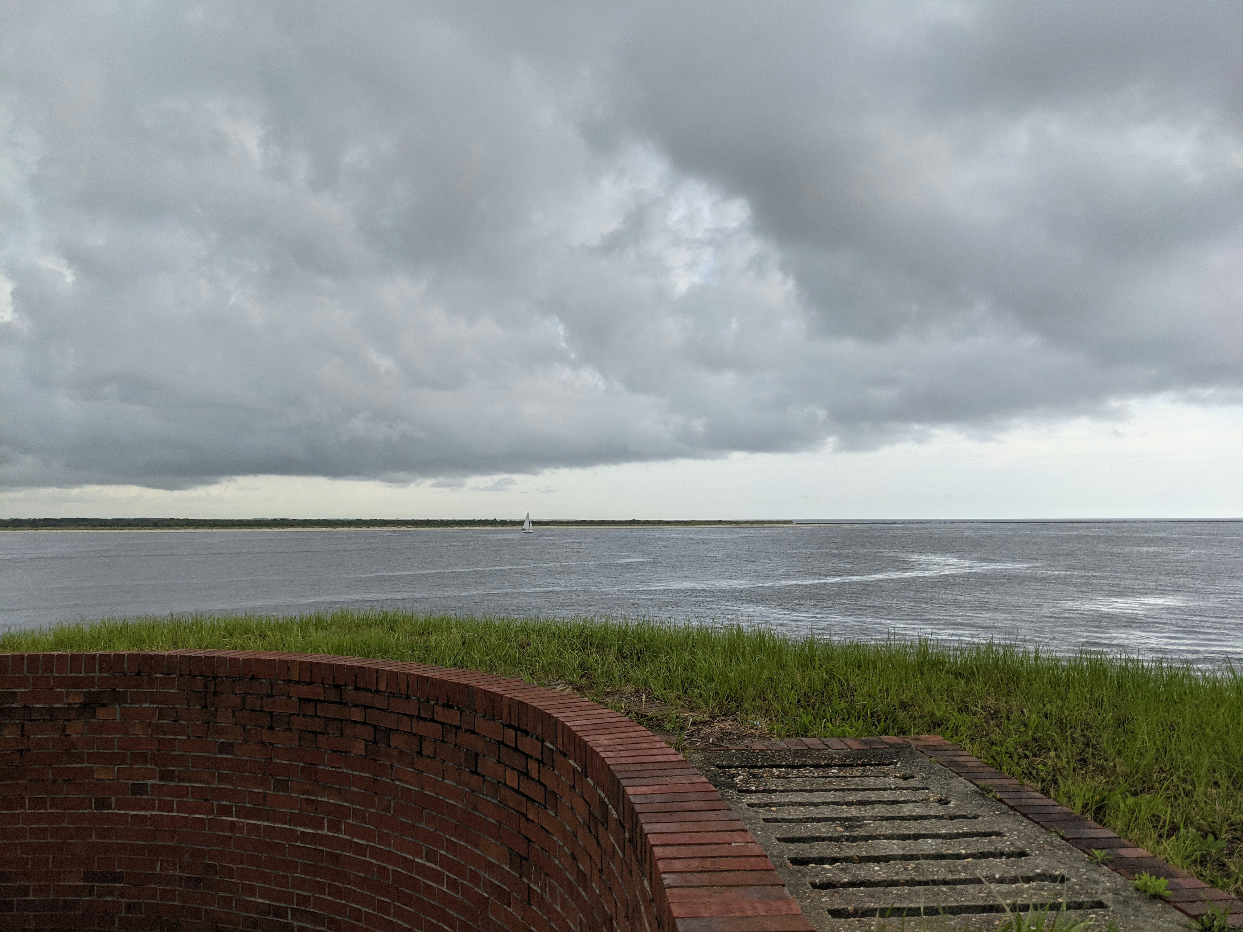 Curved Brick Wall Framing a Distant Beacon Under Stormy Skies