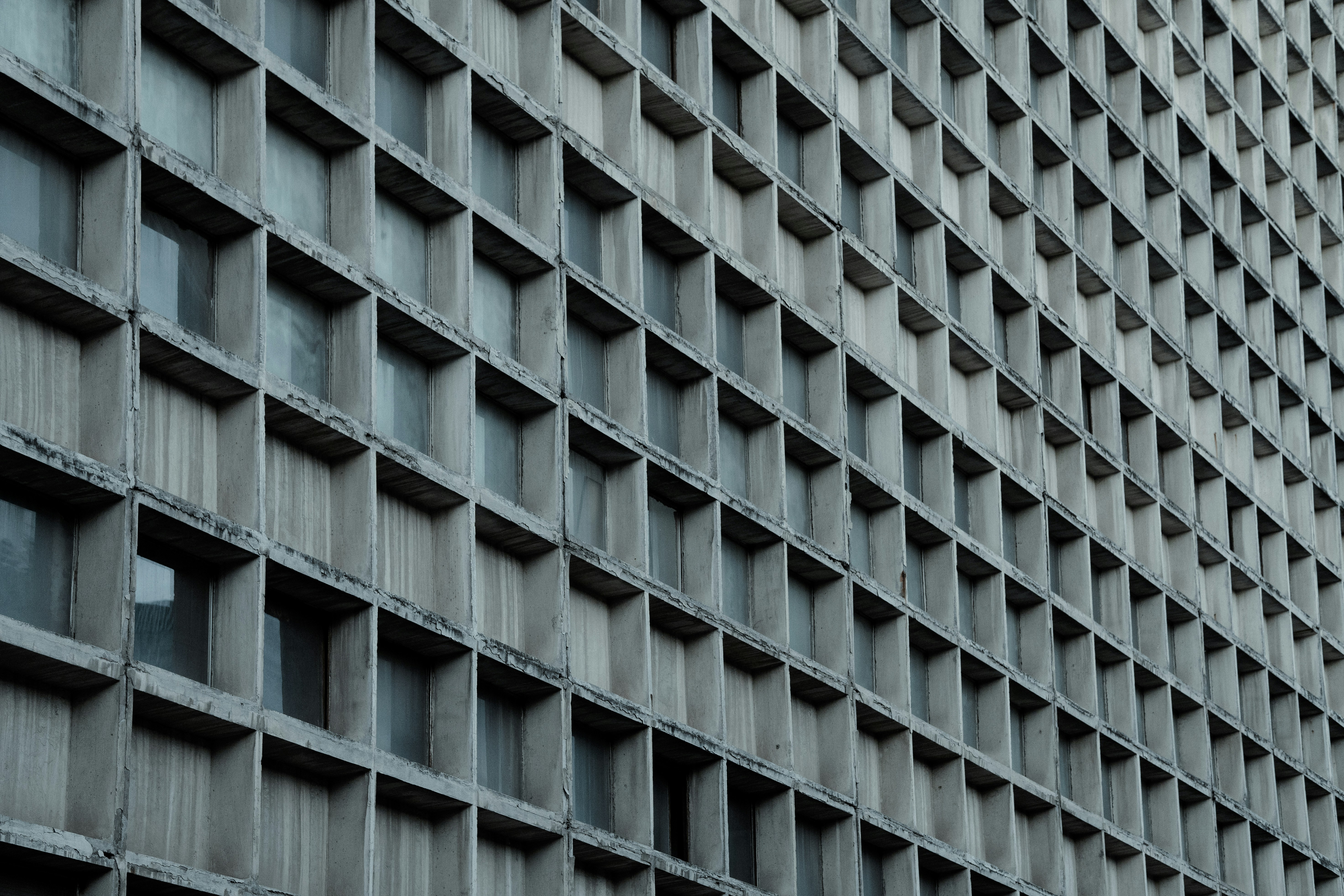 Abstract view of a concrete building facade showcasing a grid of square windows. The arrangement highlights the interplay of light and shadow across the surface.