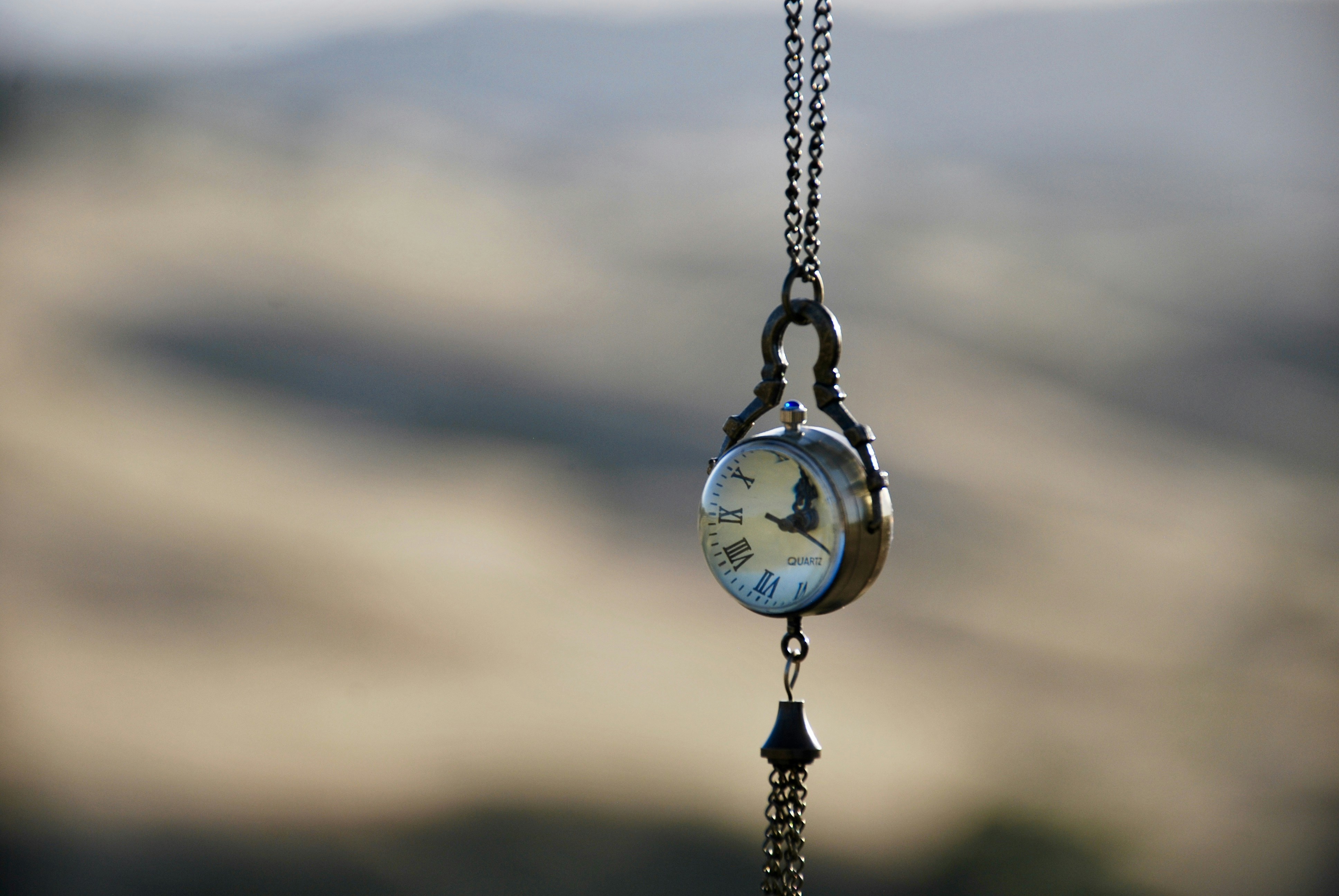 Time Pendant: A lone pocket watch suspended against a sunlit desert backdrop