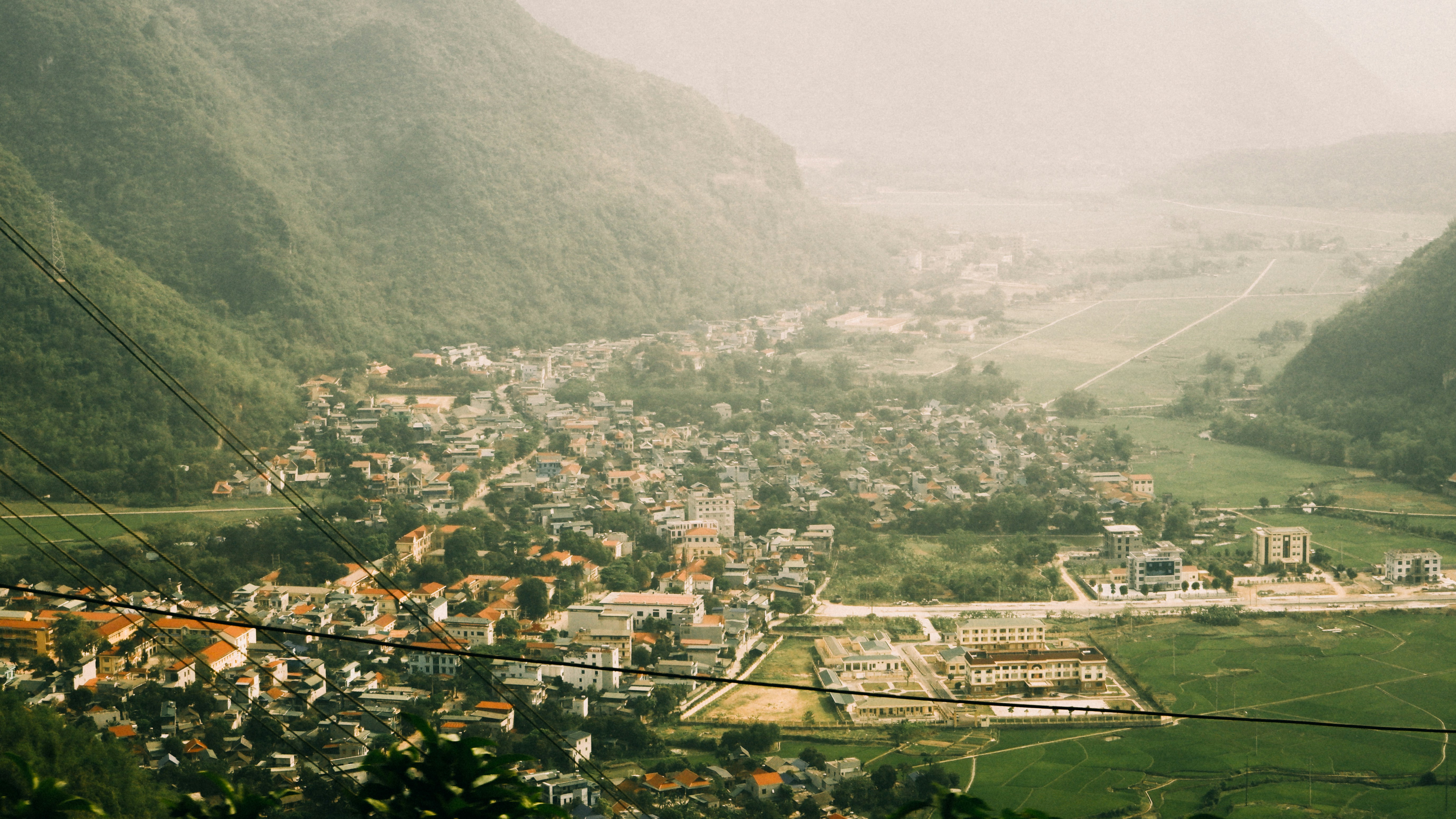 Aerial view of a tranquil village surrounded by lush mountains, showcasing a blend of traditional architecture and green landscapes.