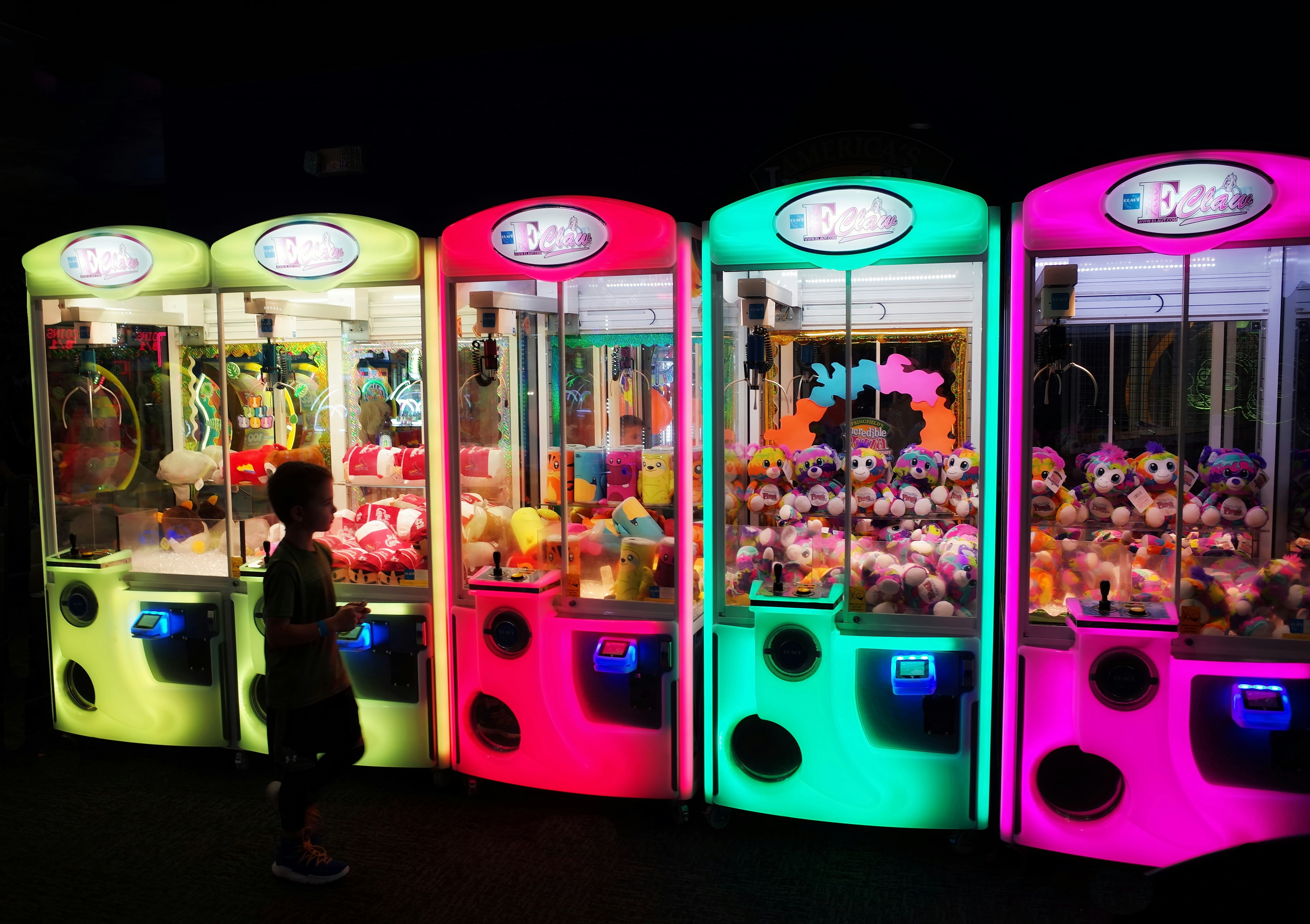 A young boy standing in front of a row of brightly lit vending machines ...