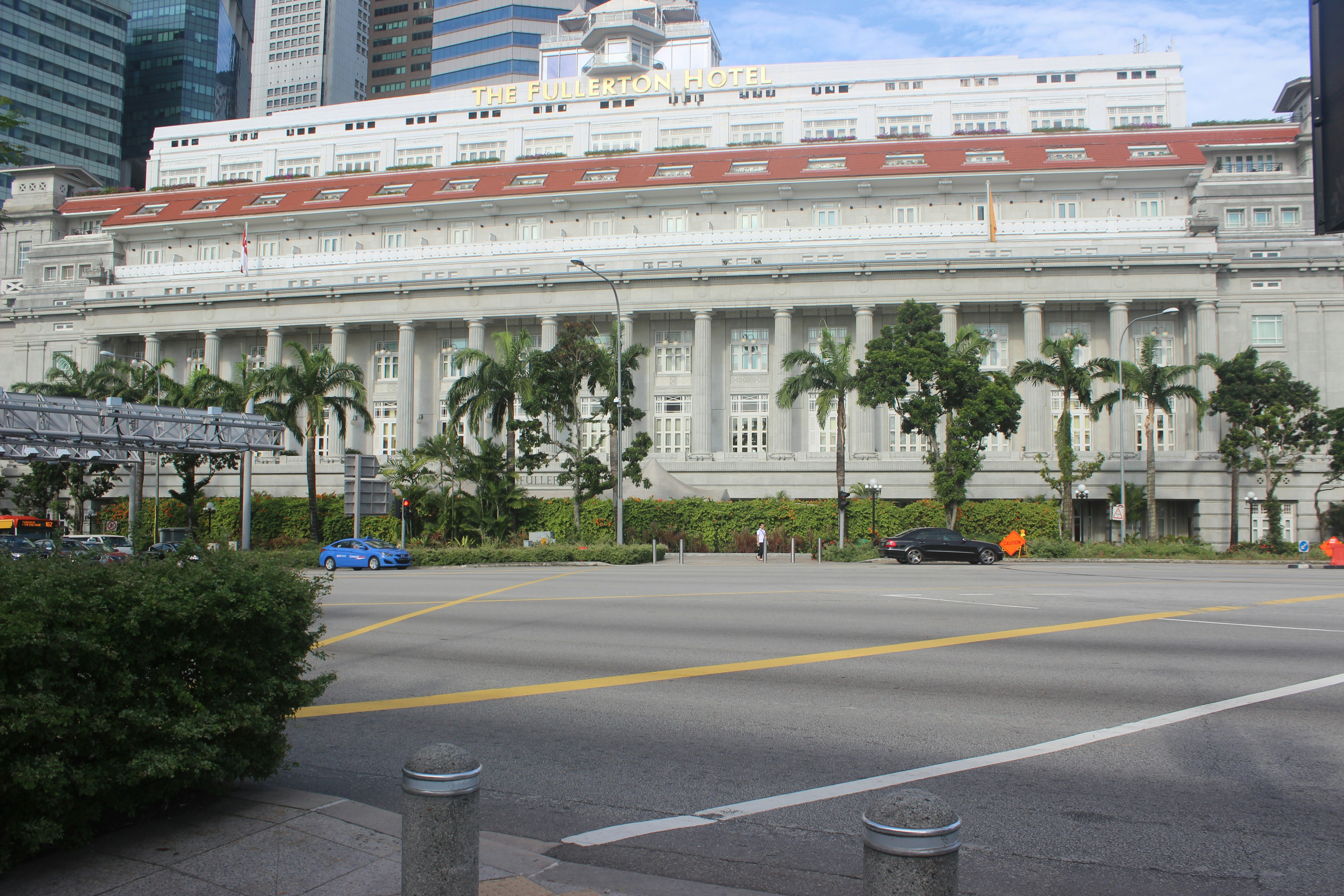 White building with palm trees lining the front, set against a backdrop of modern skyscrapers.