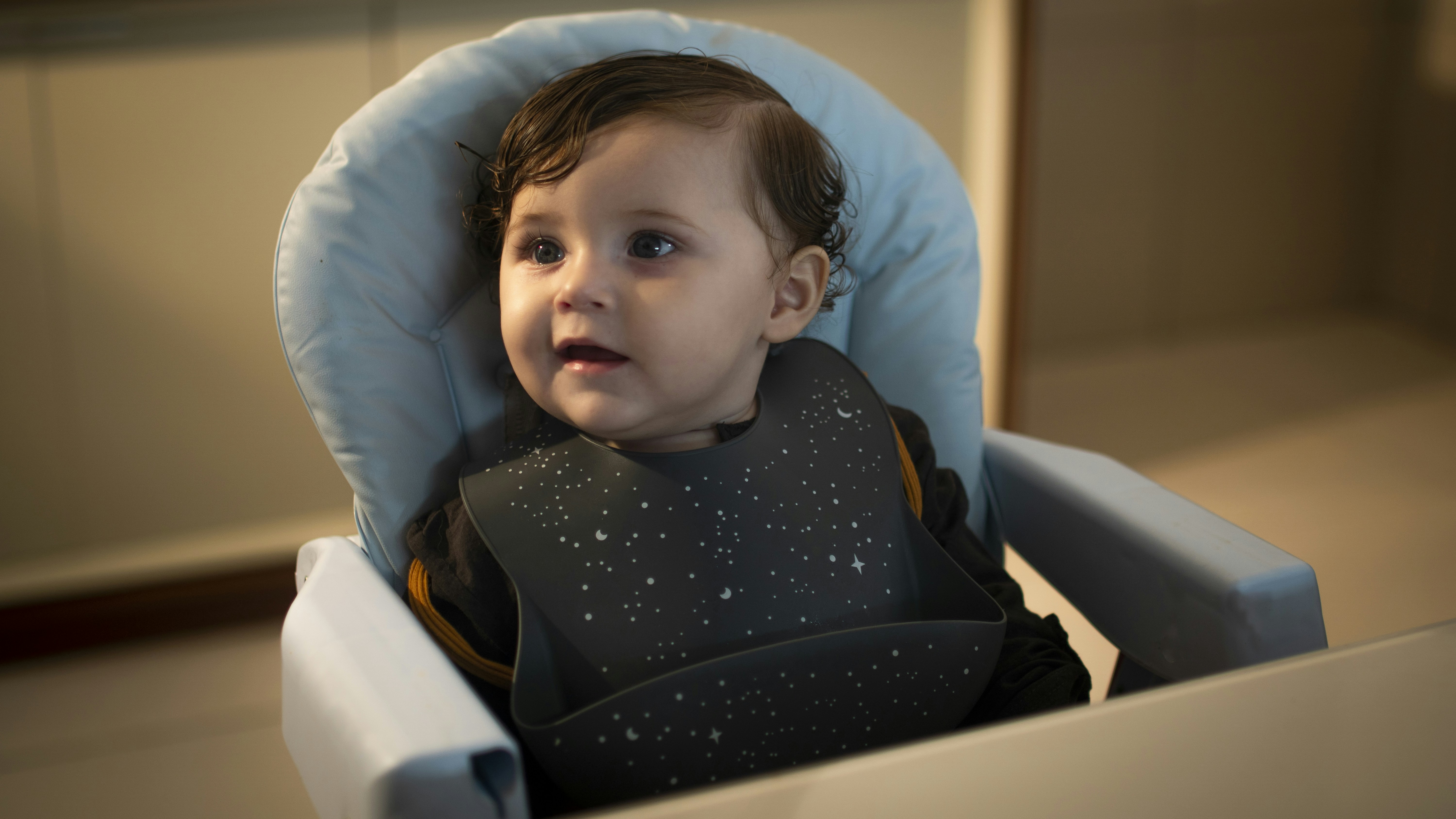 Starry Bib, Soft Gaze: A Baby's Quiet Moment in a Blue High Chair