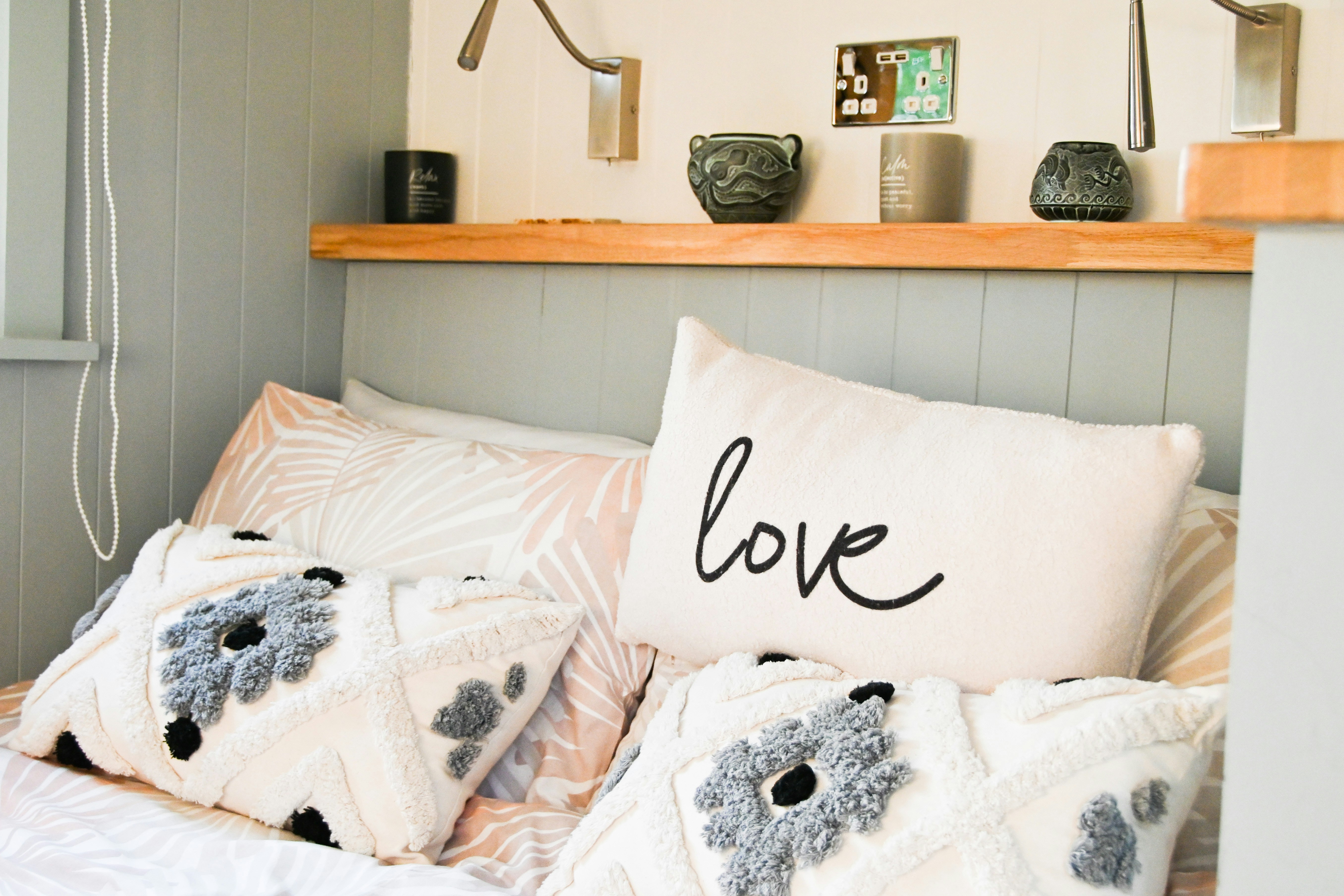 Stylish bedding with decorative pillows featuring a handwritten 'love' accent, set against a softly colored wall and wooden shelf adorned with unique decor items.