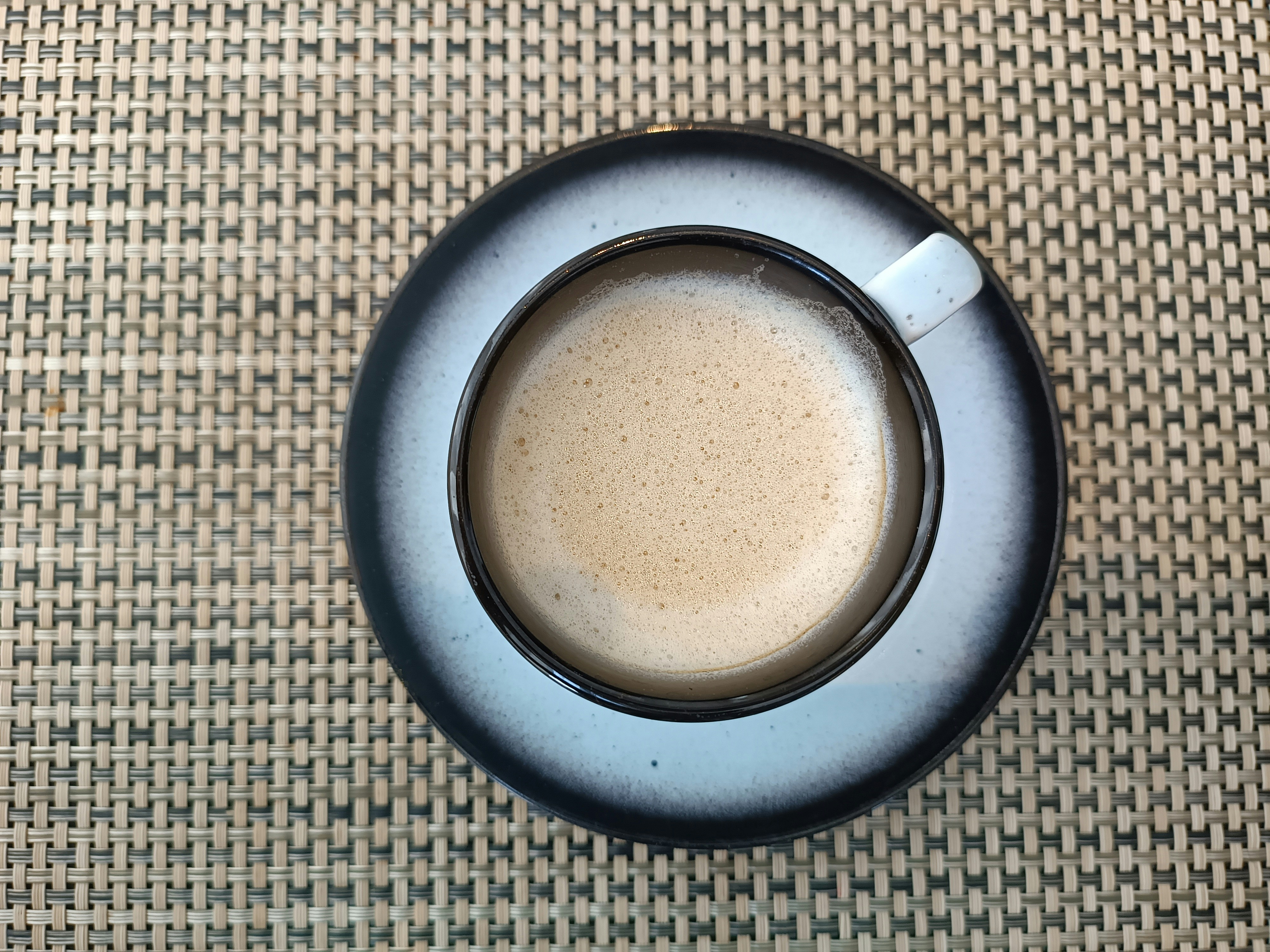 A close-up view of a coffee cup resting on a textured surface, showcasing the frothy beverage within. The minimalist composition emphasizes the simplicity and warmth of coffee culture.