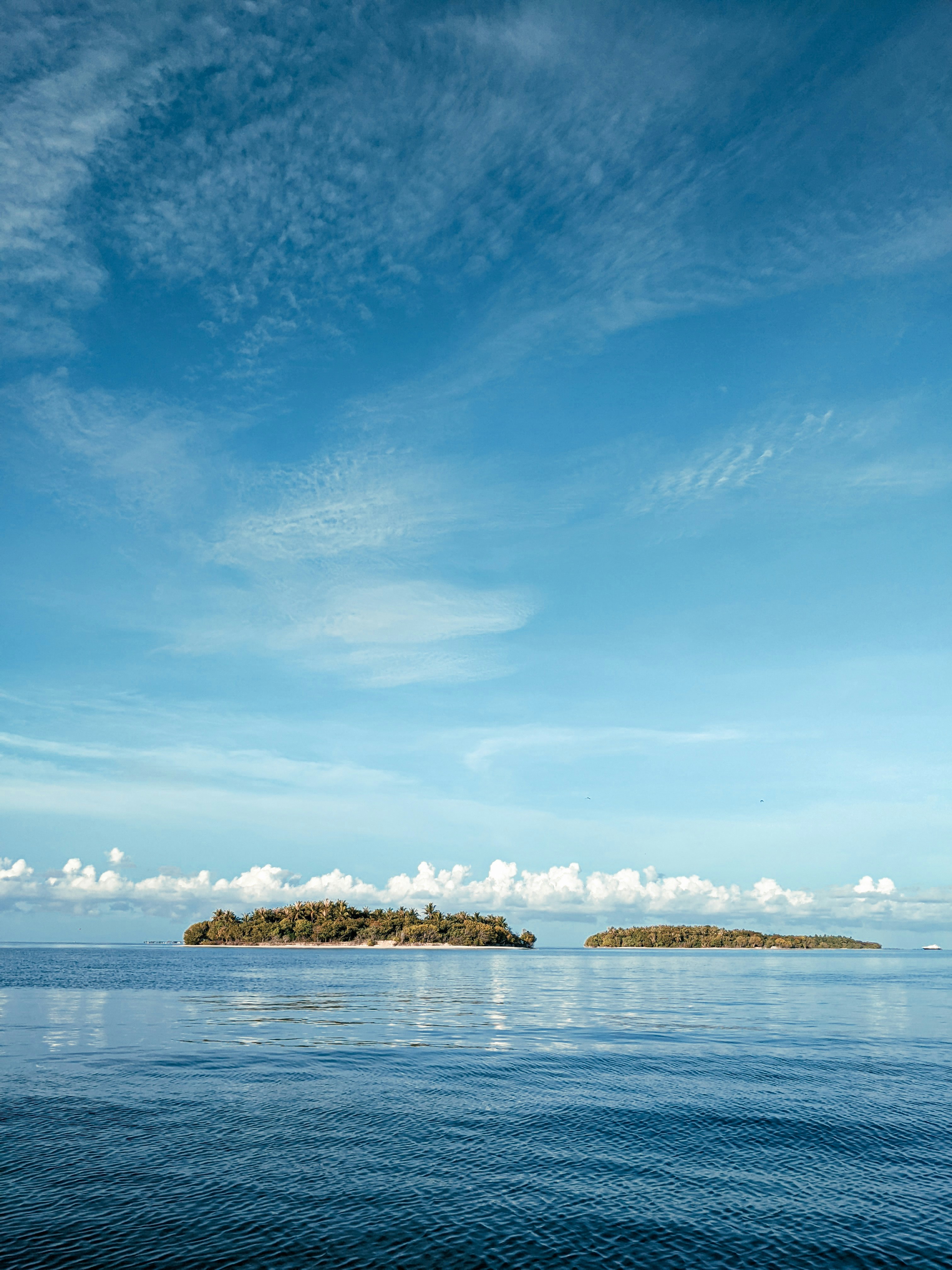 Two lush islands emerge from the serene waters under a vast blue sky, reflecting tranquility and natural beauty.
