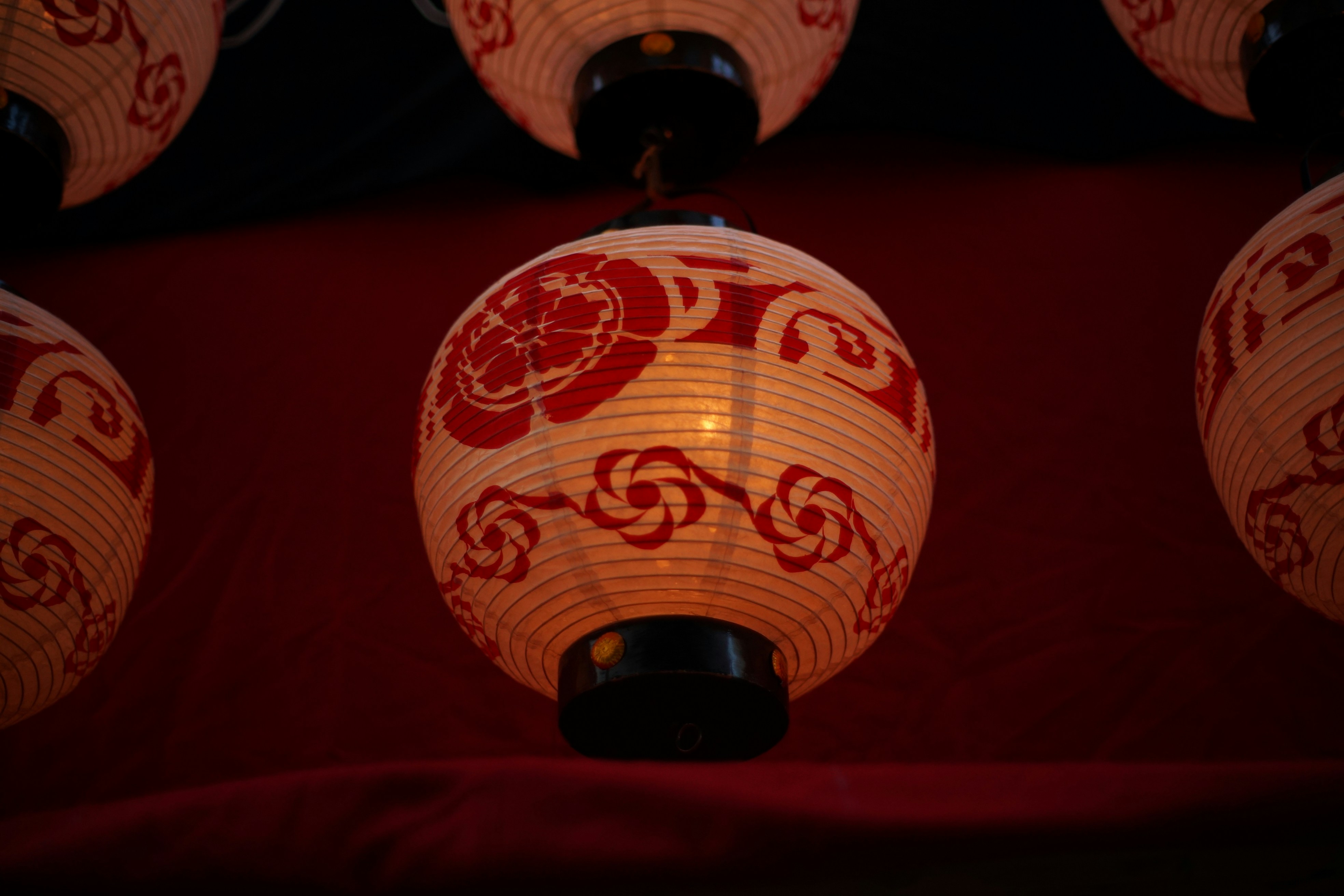 A beautifully designed paper lantern with intricate red patterns, suspended against a dark backdrop, showcasing traditional craftsmanship.