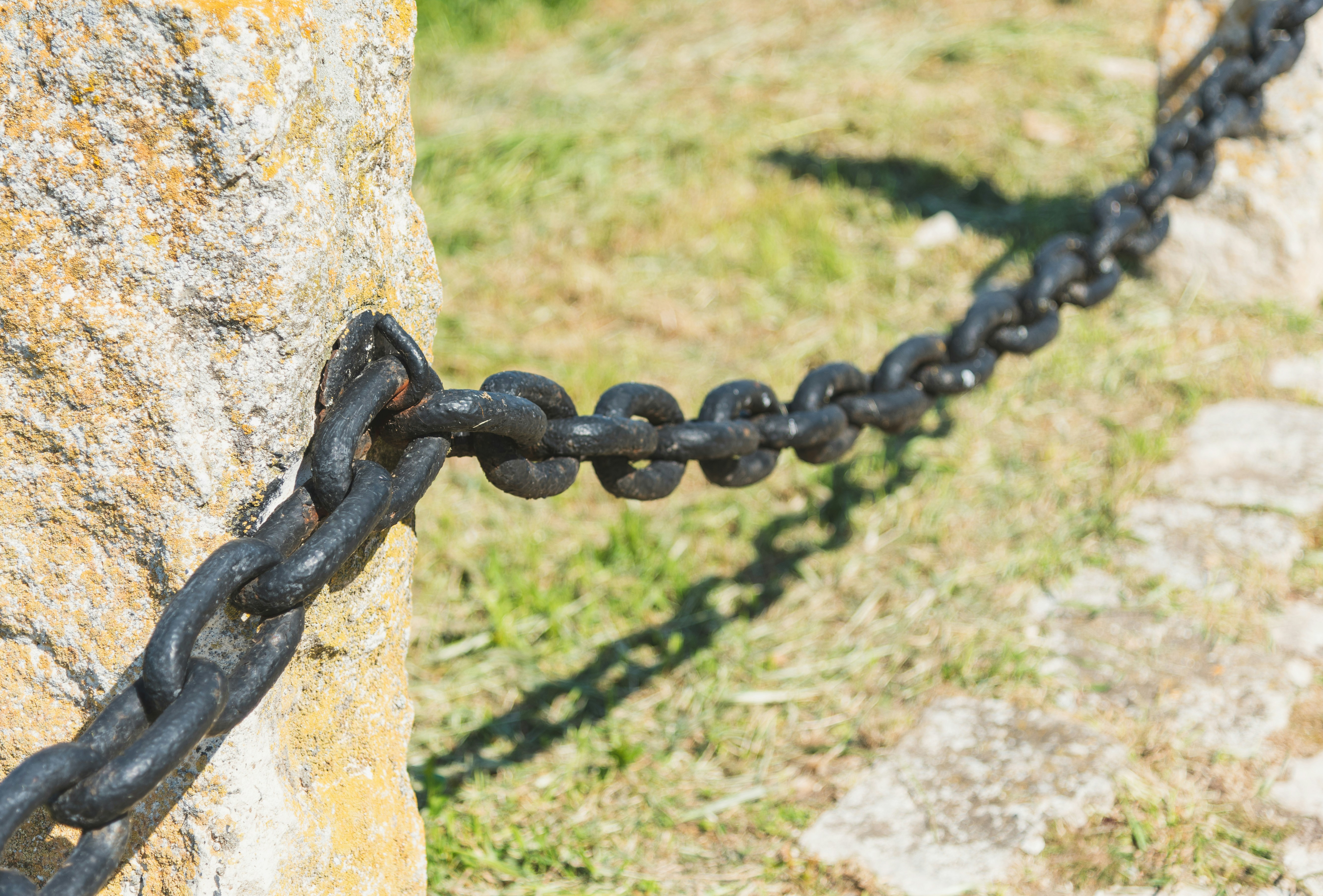 Close-up of a weathered chain linked to a stone post, highlighting textures and contrasts in a natural setting.