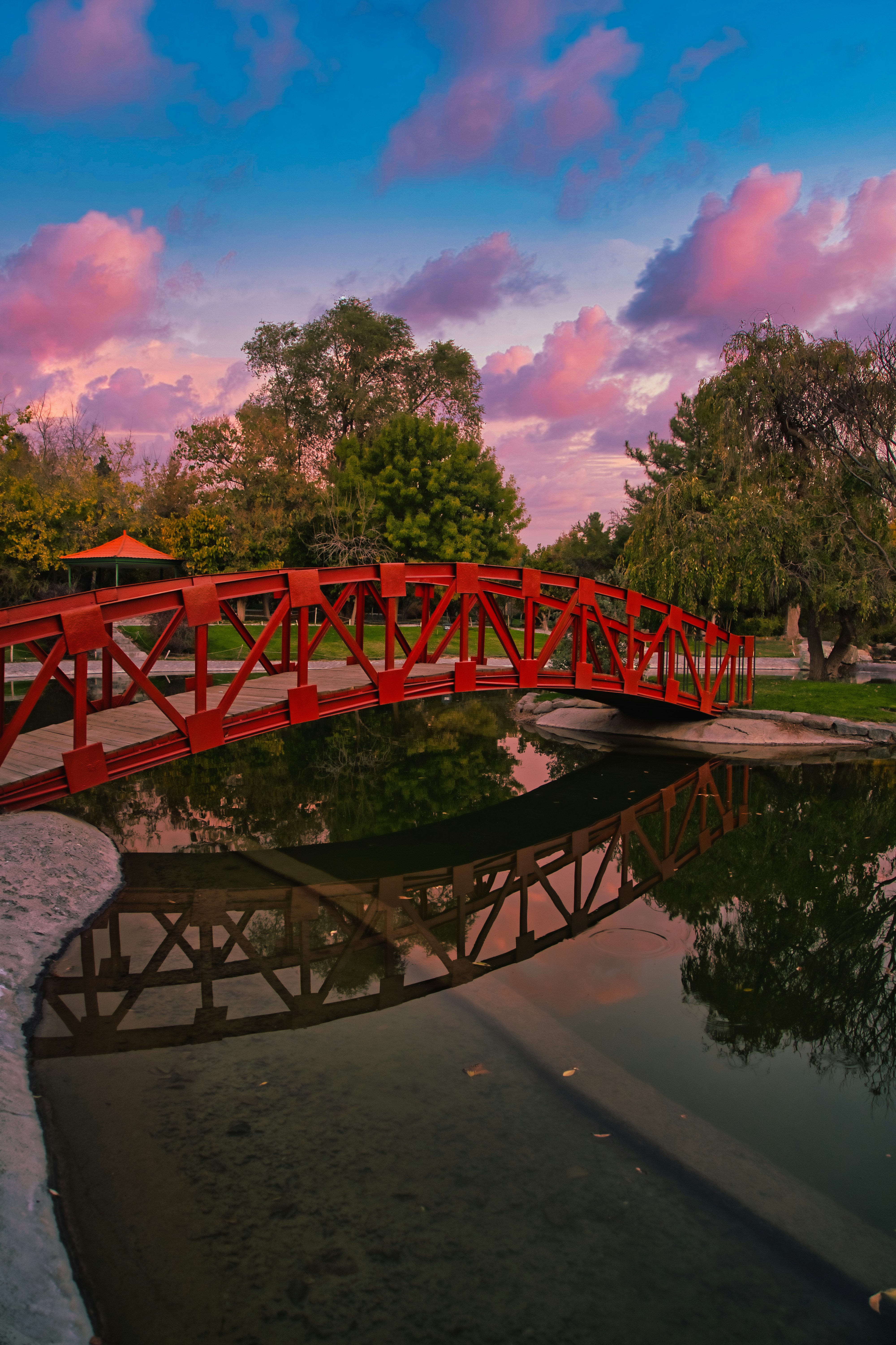 Crimson Span: A Red Bridge Framing a Reflective Pond at Sunset